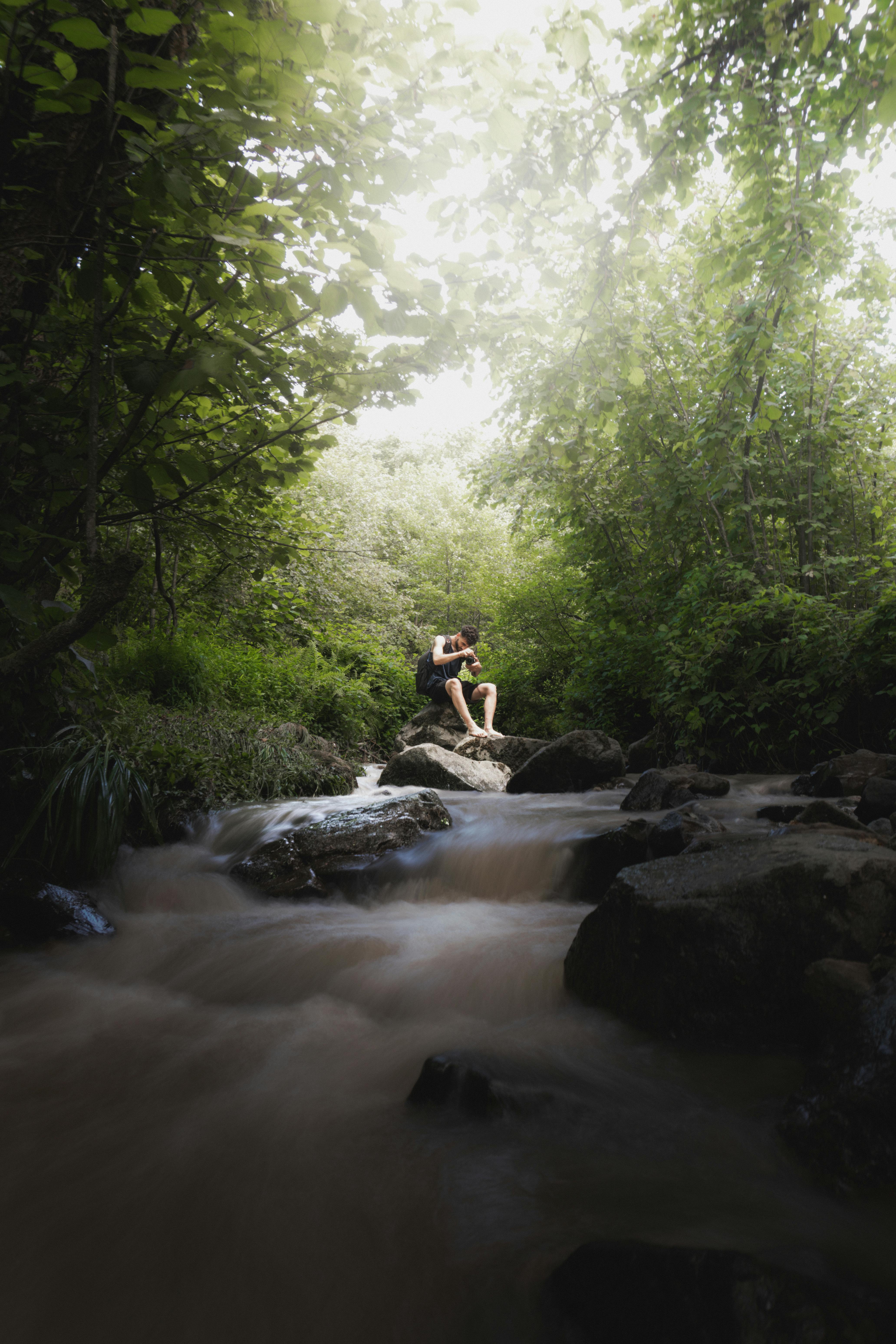 A man sitting on a rock in the middle of a stream · Free Stock Photo