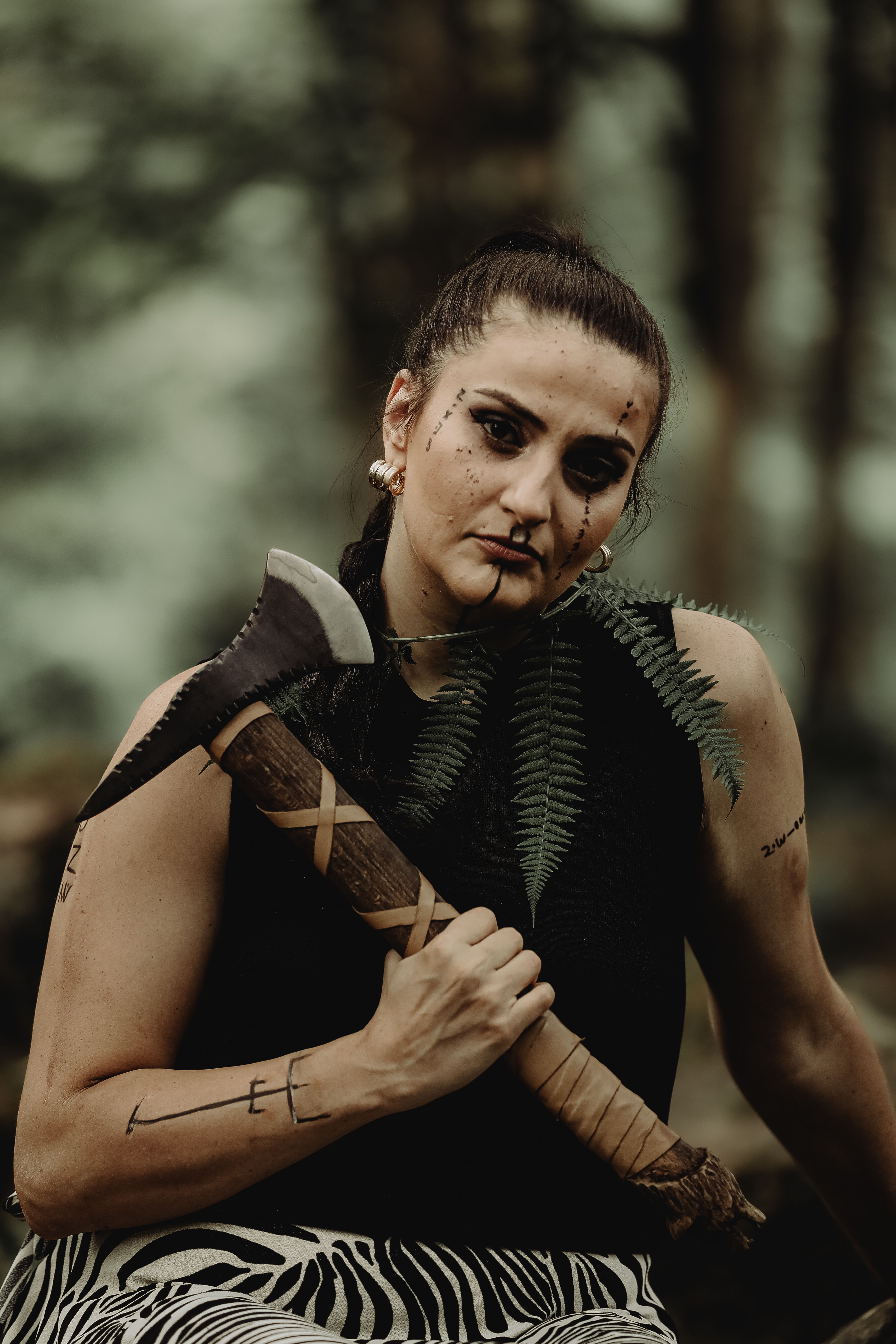 A woman with tattoos holding an axe in the woods · Free Stock Photo