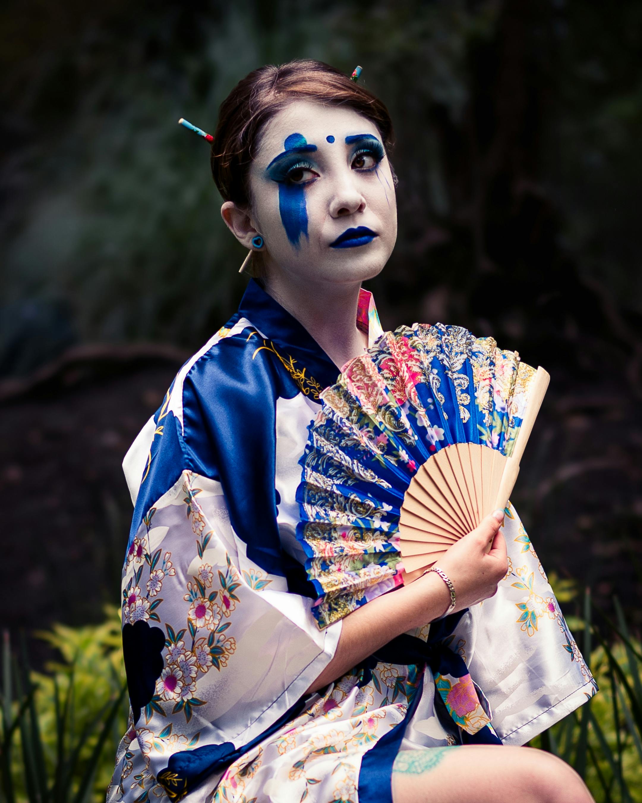 A woman with blue face paint holding a fan · Free Stock Photo