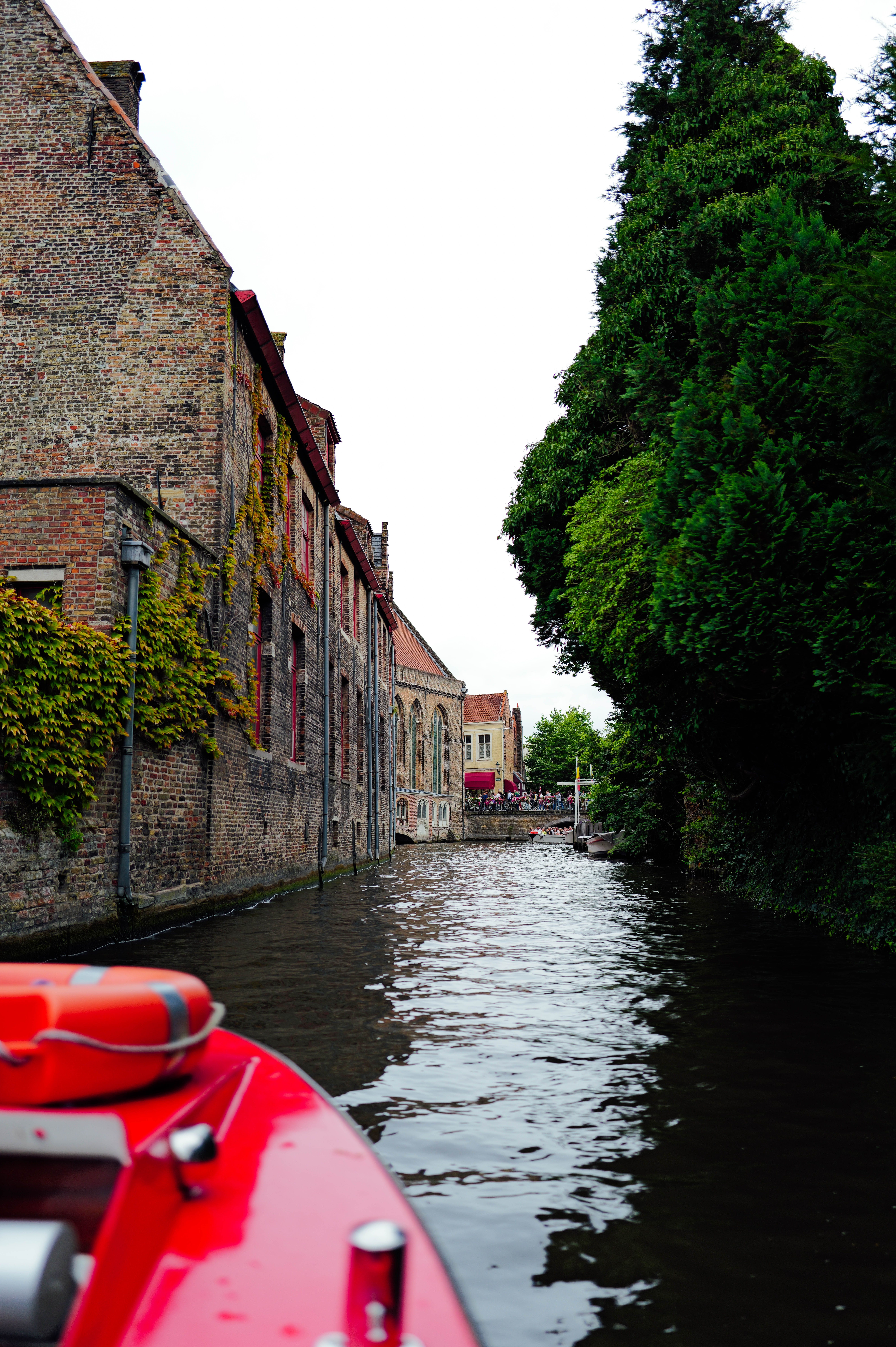 A red boat is traveling down a canal in a small town · Free Stock Photo