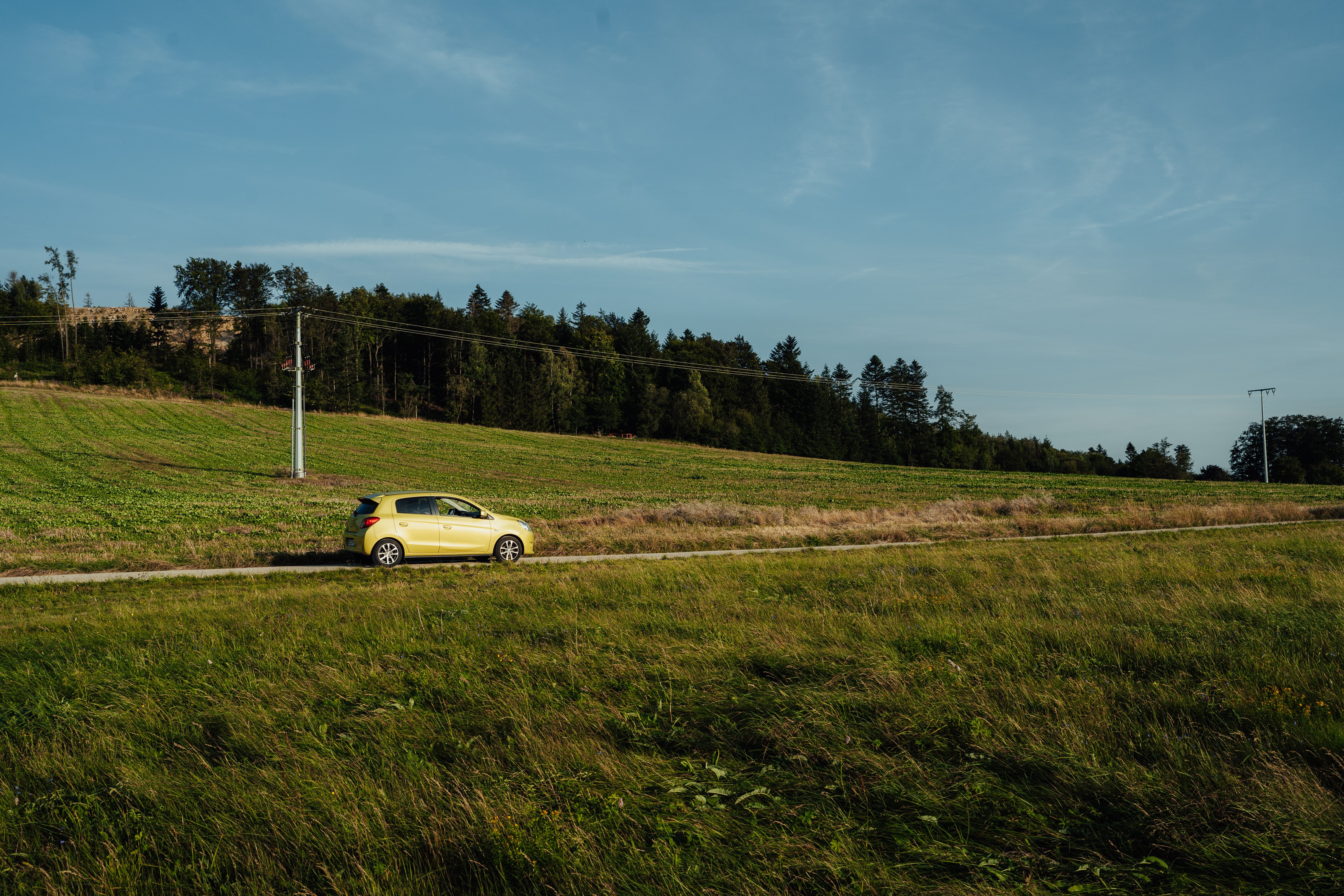 A yellow car driving down a road in a field · Free Stock Photo