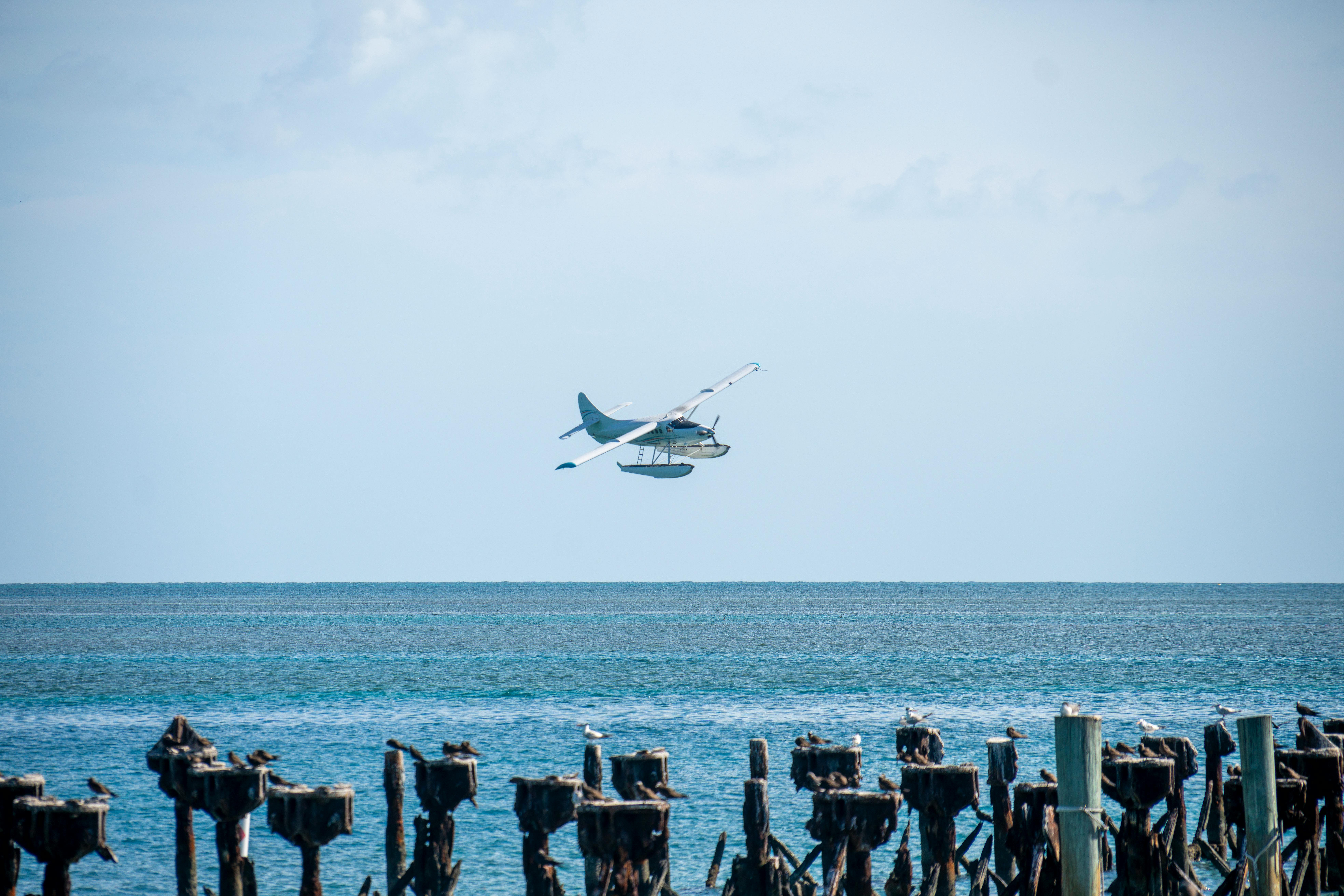 A small plane flying over the ocean near some poles · Free Stock Photo