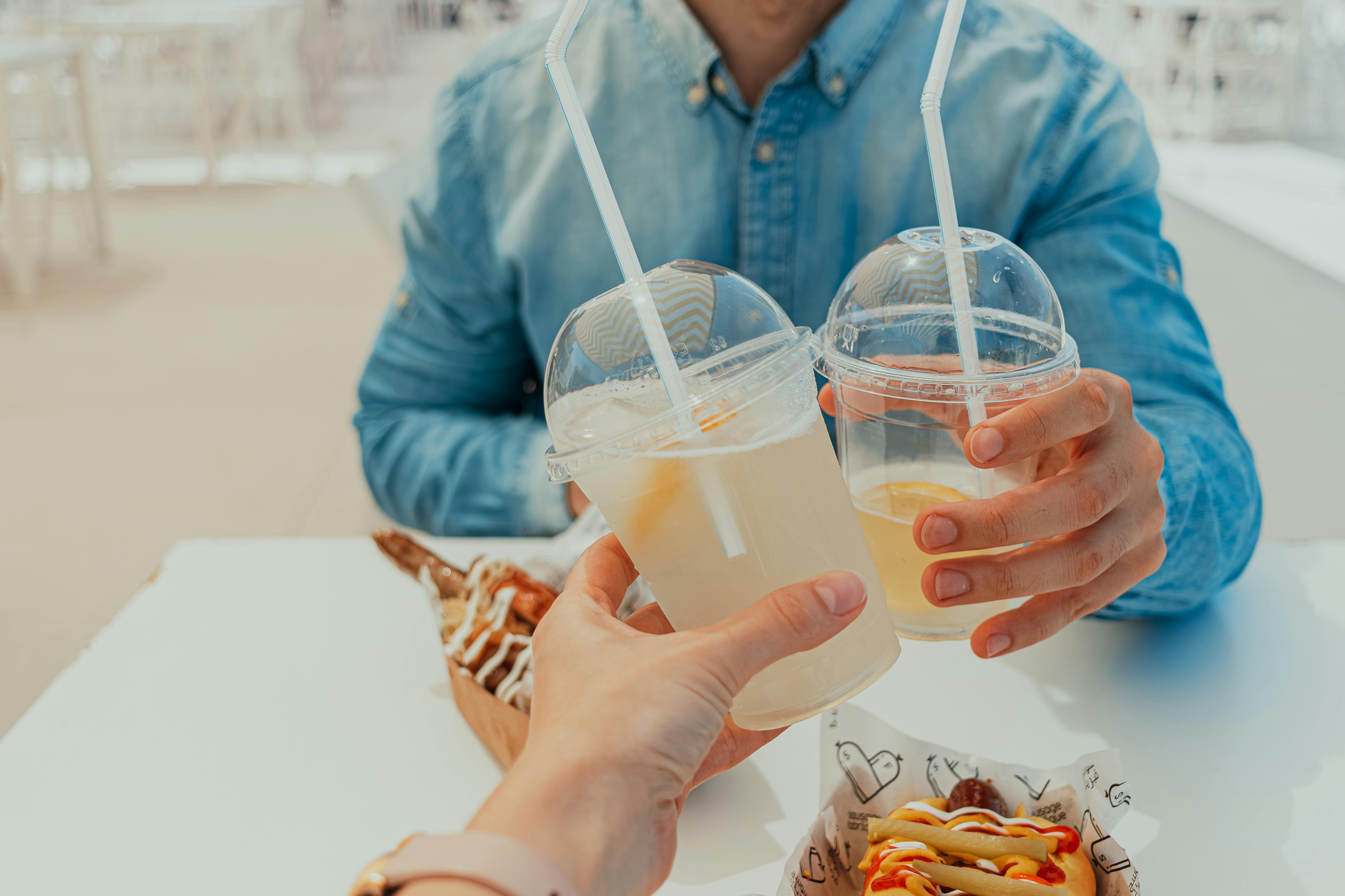 Two people clinking plastic cups of lemonade over a table with hot dogs ...