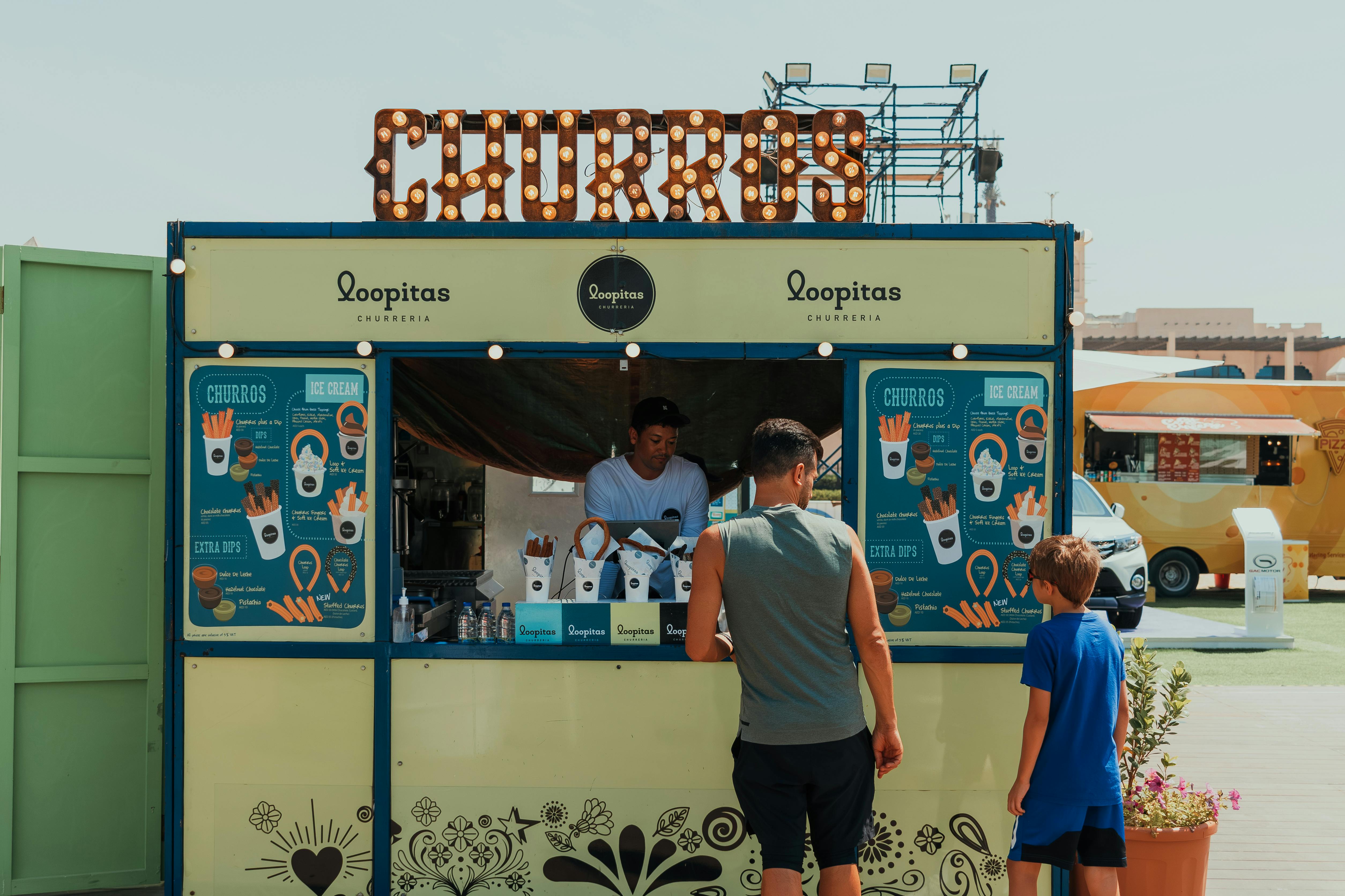 Customers at a Churros outdoor stand kiosk ordering snacks on a sunny ...