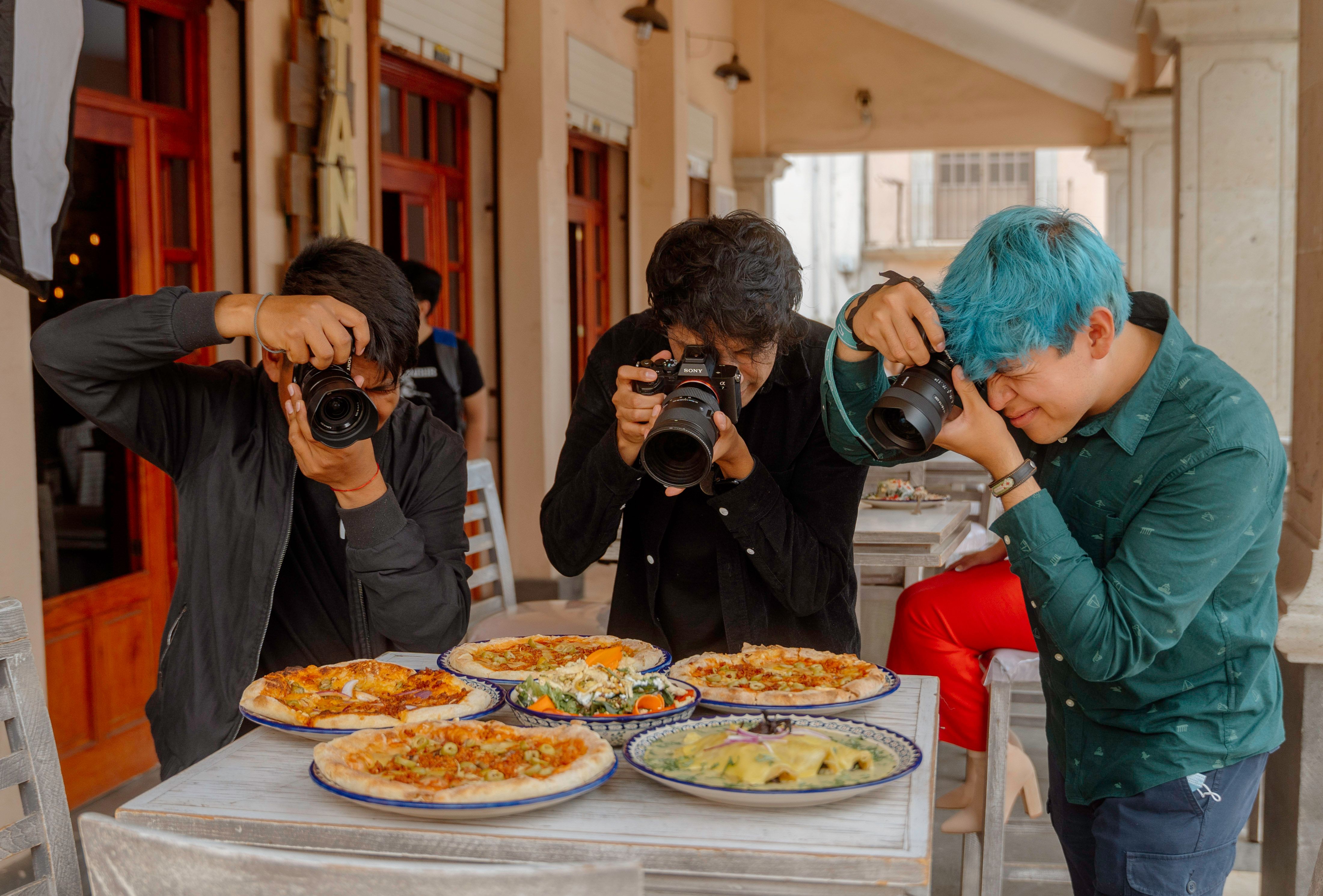 Three people taking pictures of food at a table · Free Stock Photo