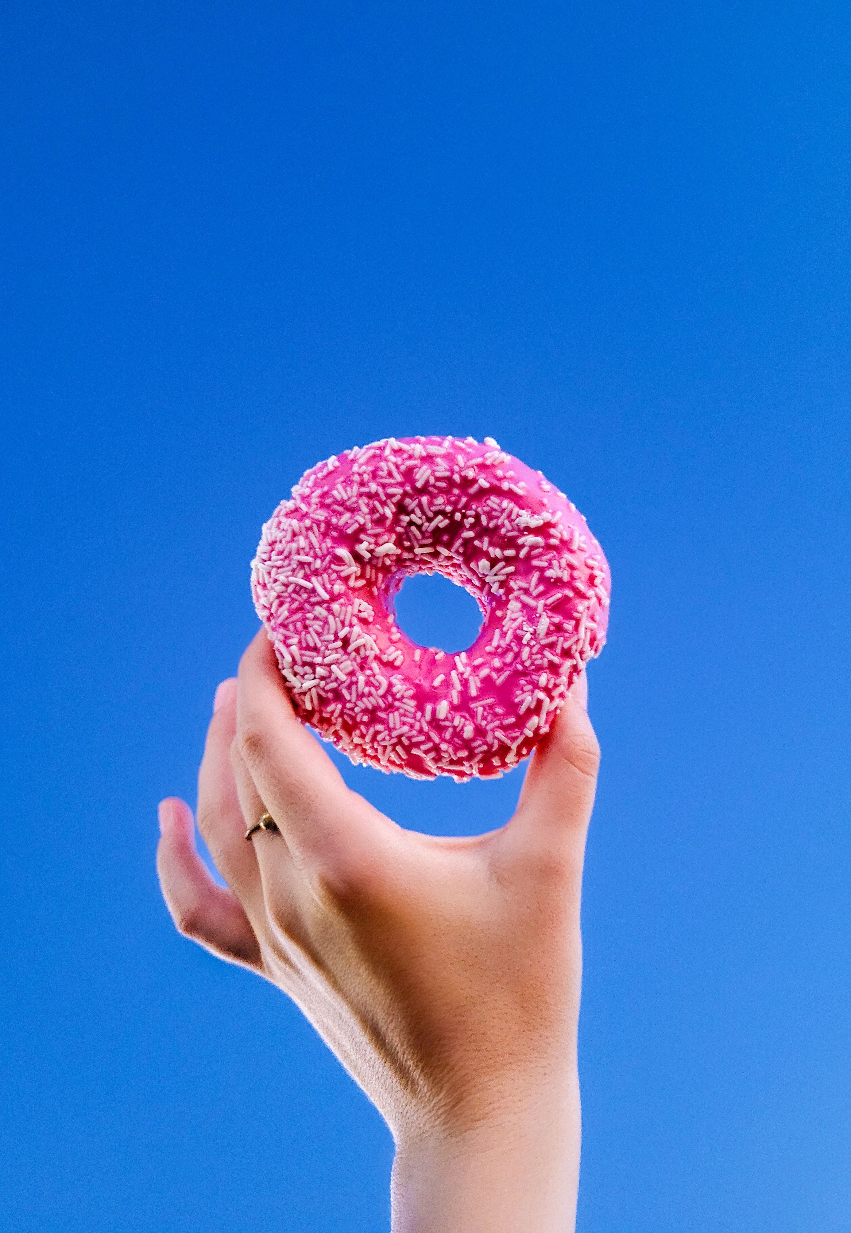 A person's hand holding a pink donut · Free Stock Photo