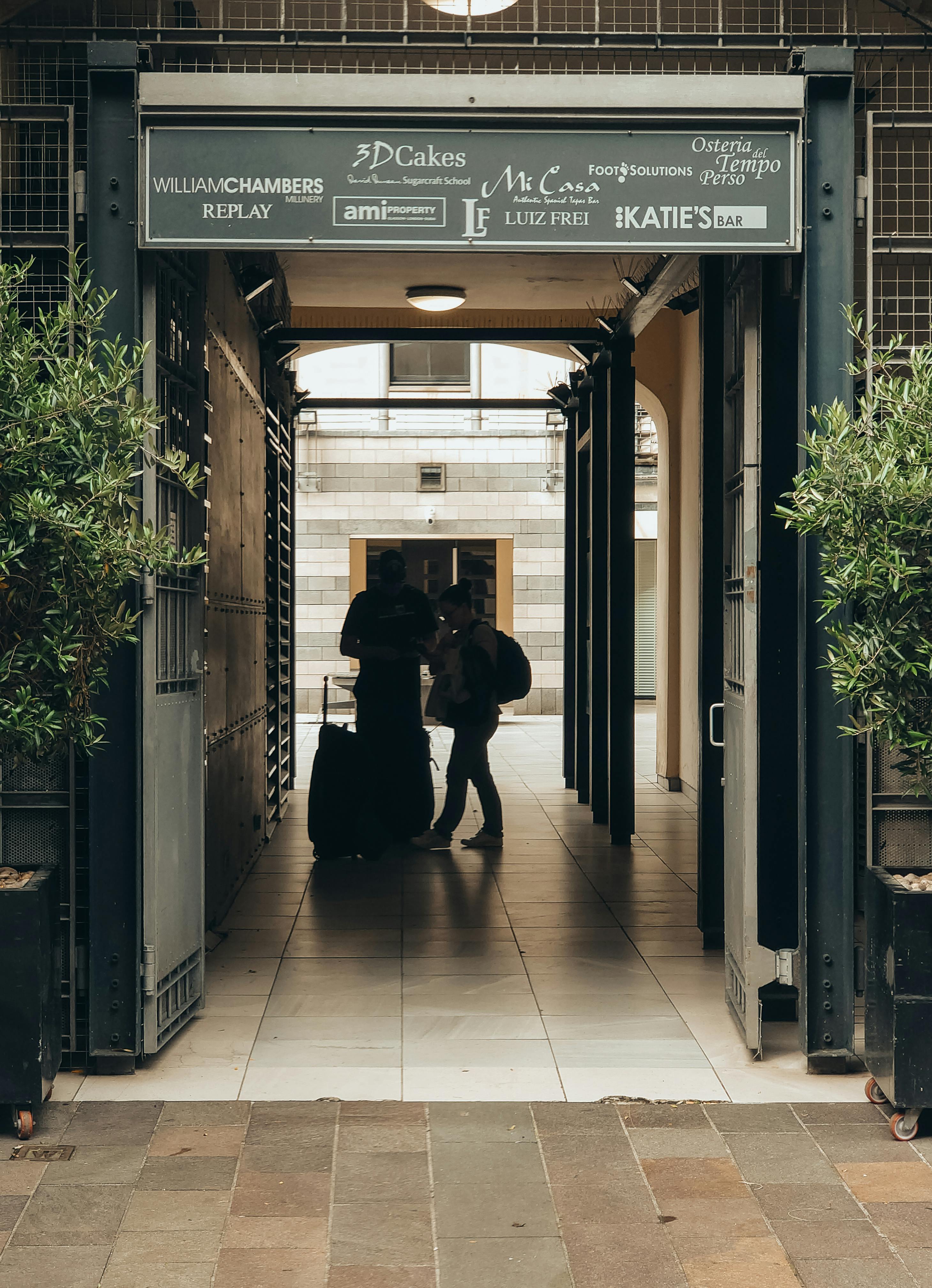 A man and woman walk through an entrance to a building · Free Stock Photo