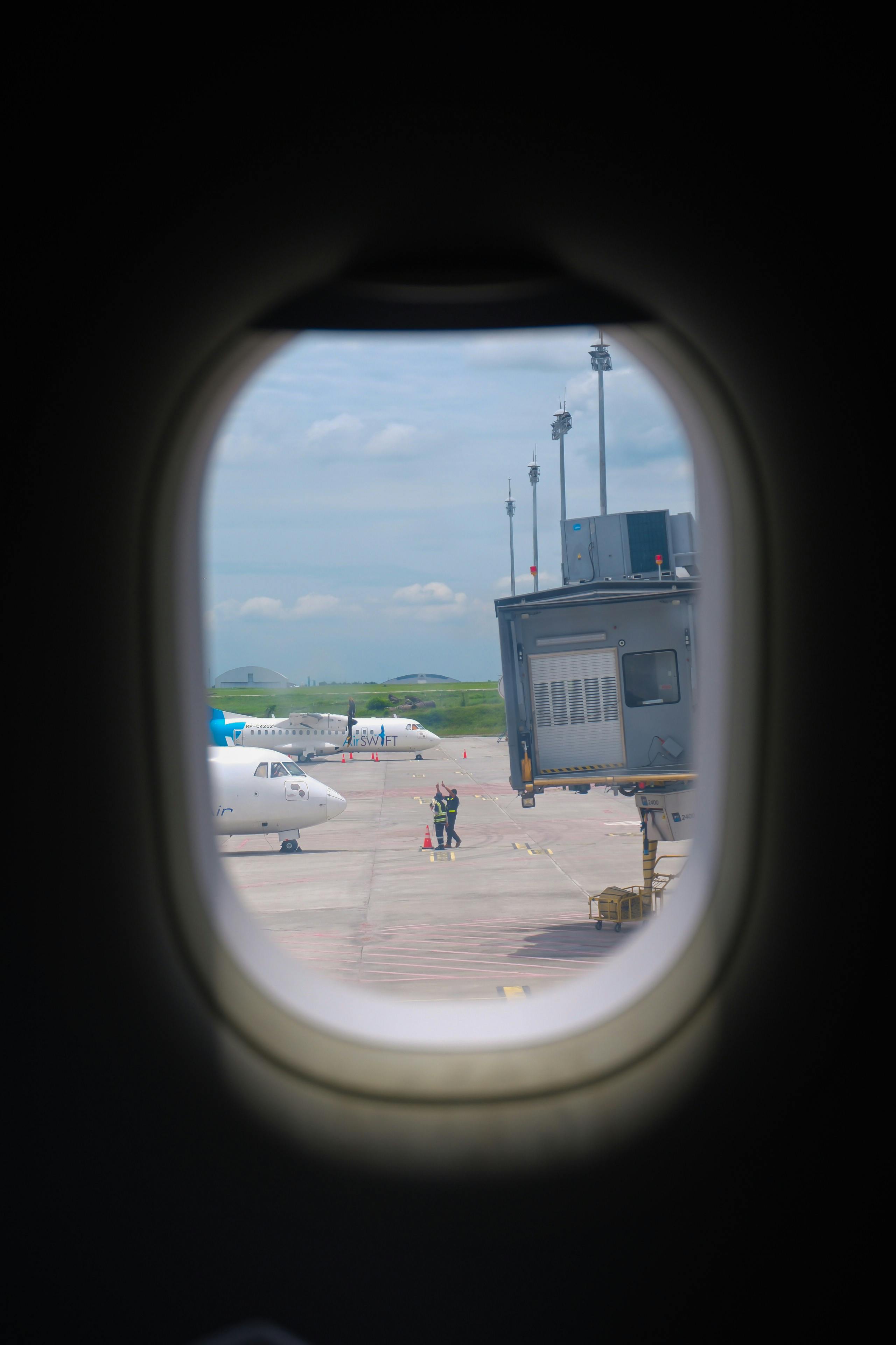A view of an airplane window looking out at an airport · Free Stock Photo