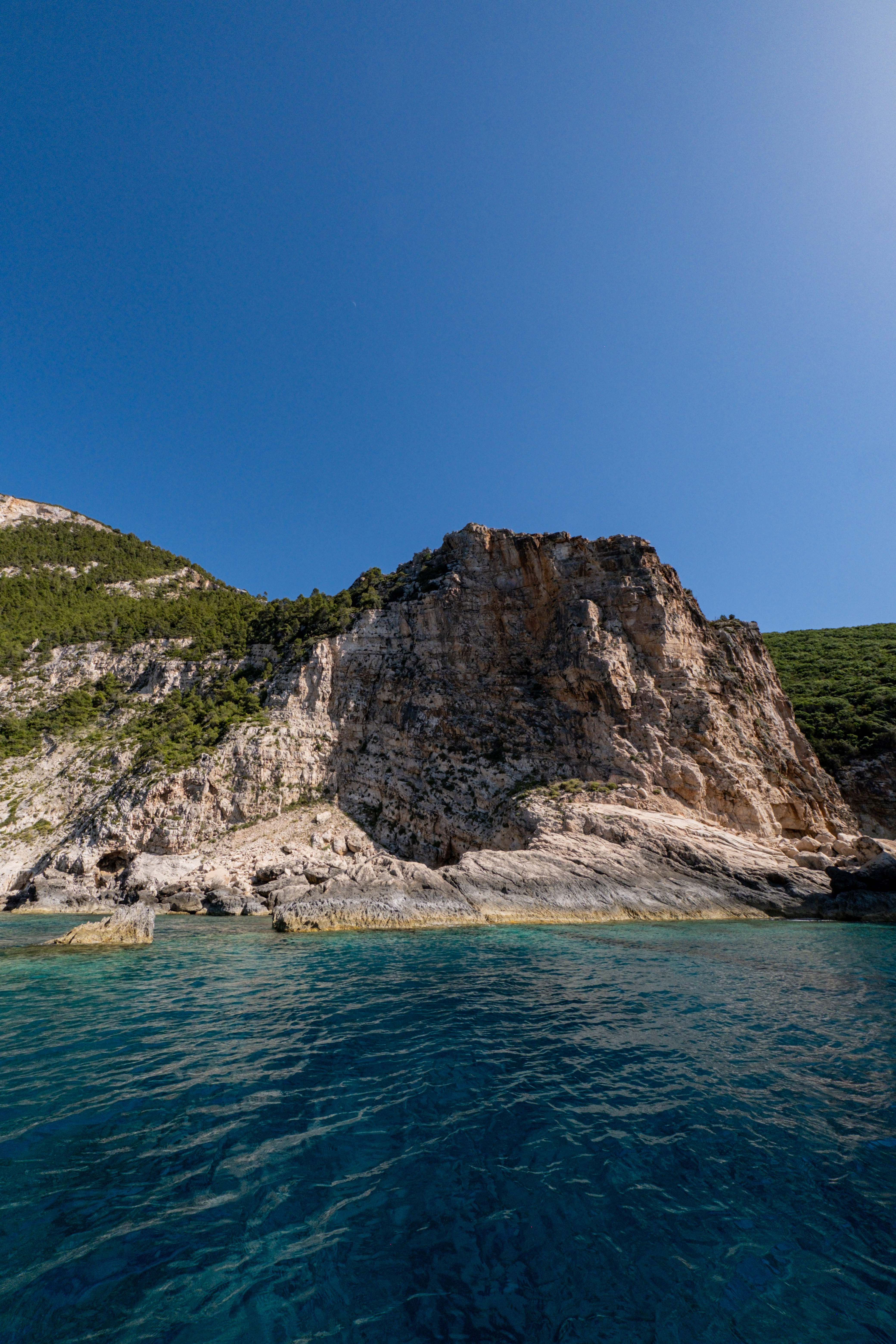 A rocky cliff with a blue sky and water · Free Stock Photo