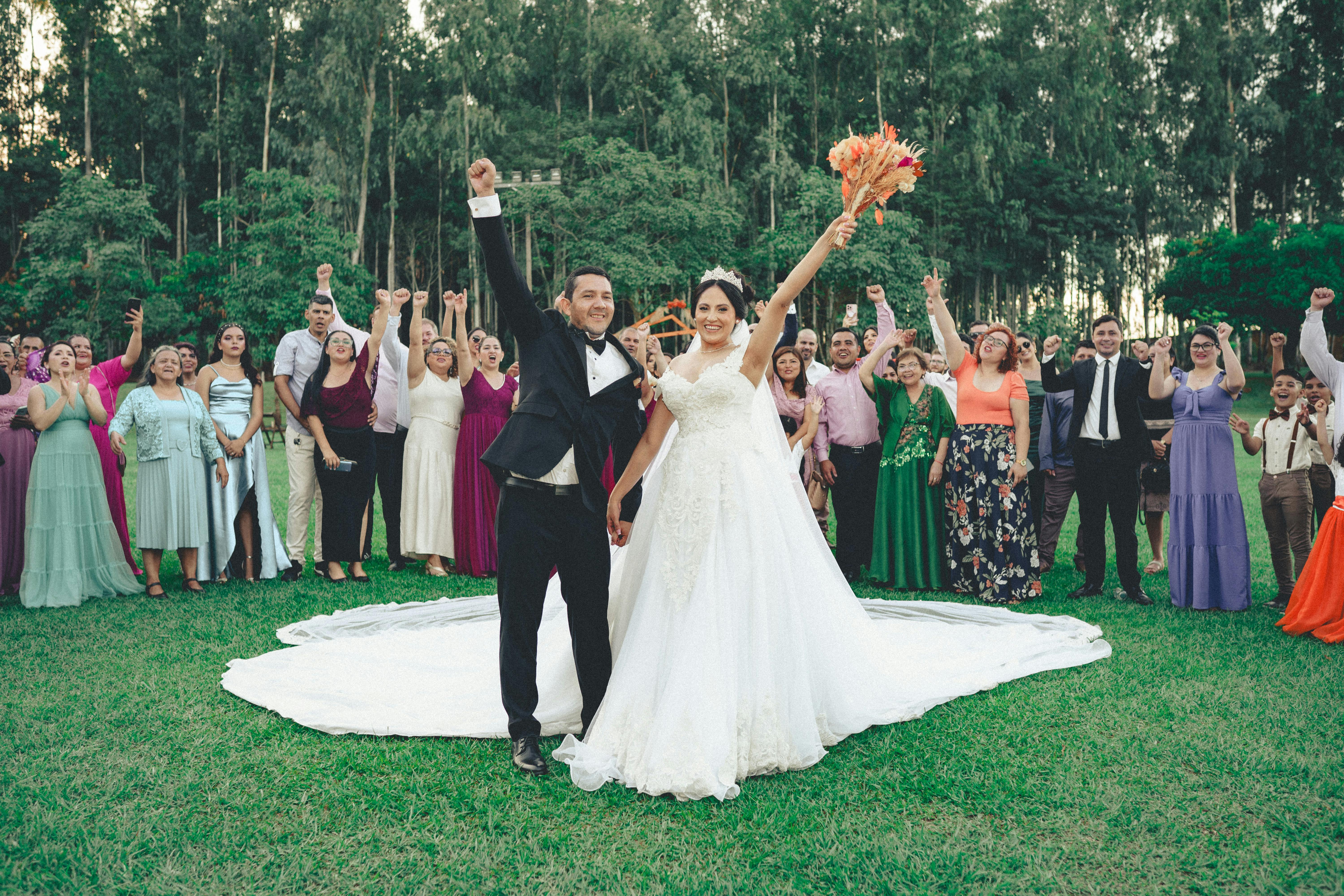 A bride and groom in the grass with their arms raised · Free Stock Photo
