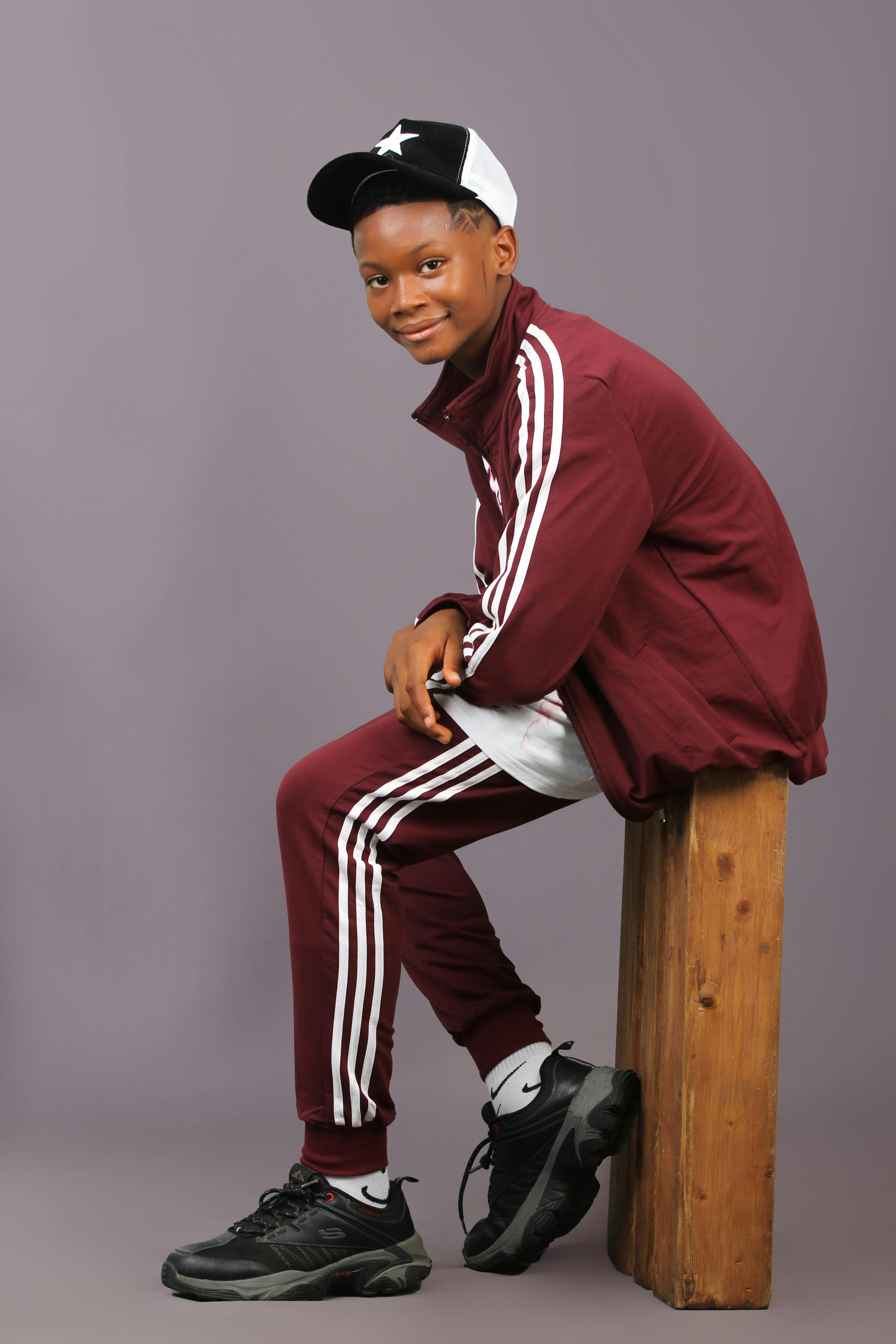 A young man in a maroon track suit sitting on a wooden block · Free ...