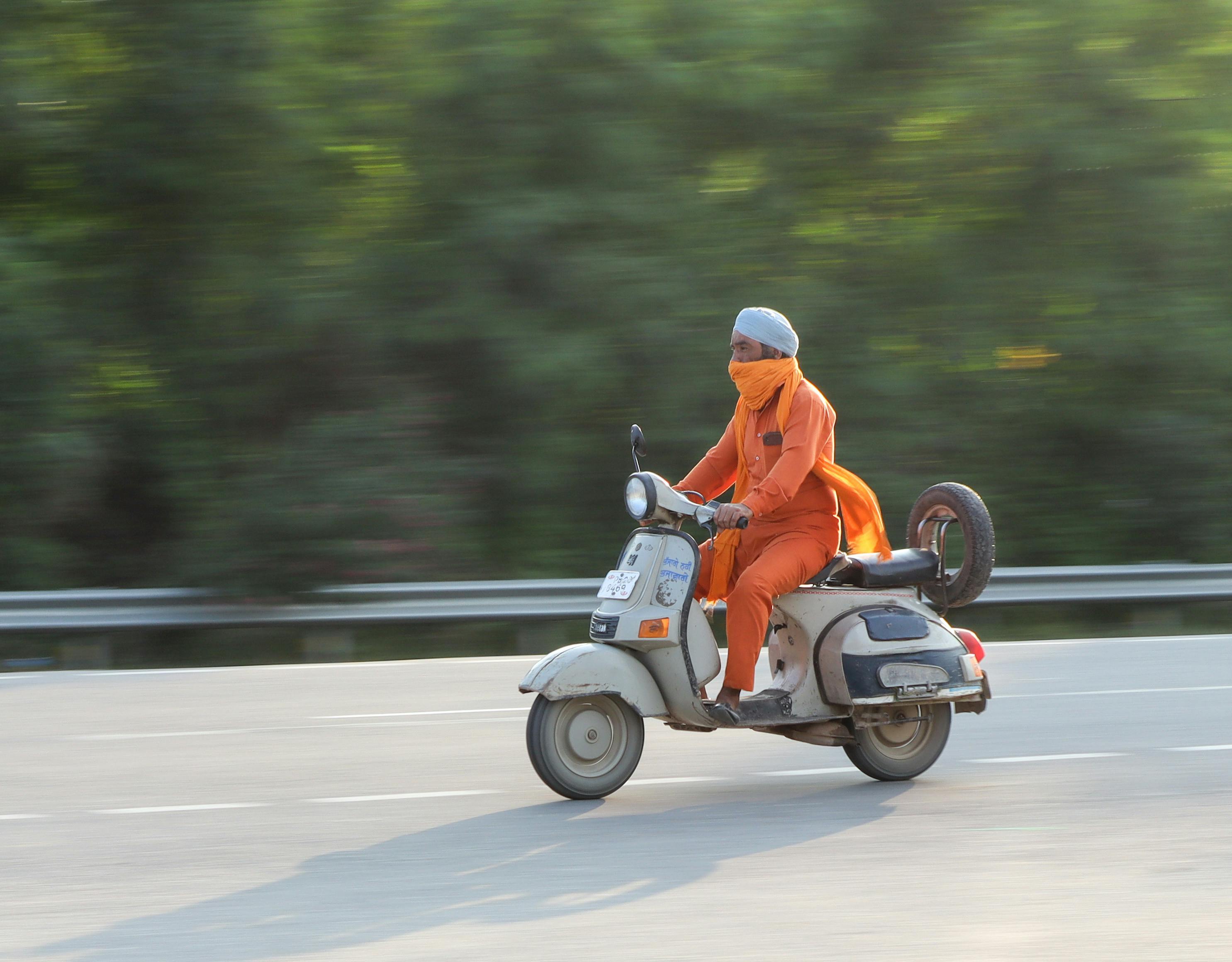 A man in orange riding a motorcycle down the road · Free Stock Photo