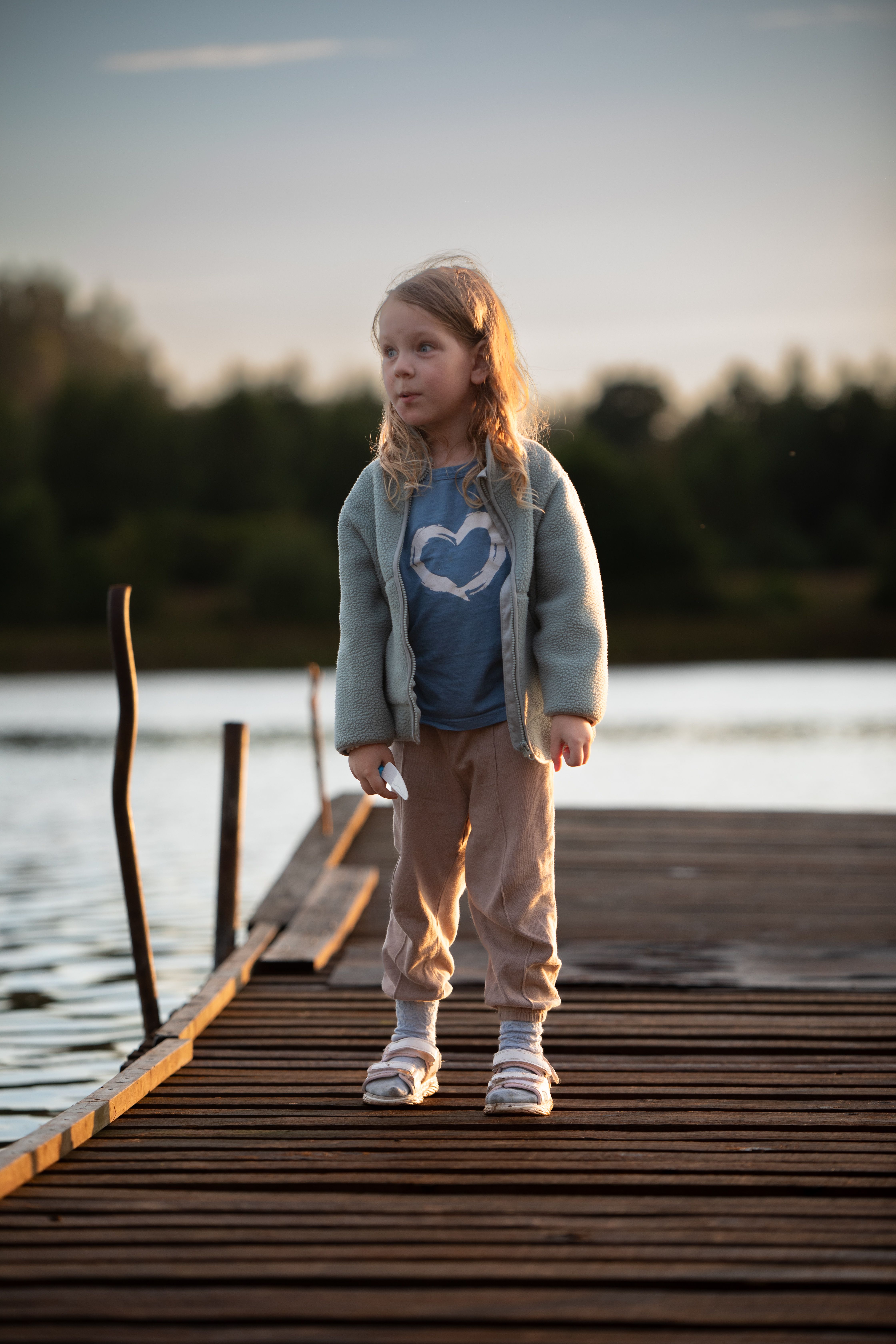 A little girl standing on a dock near water · Free Stock Photo