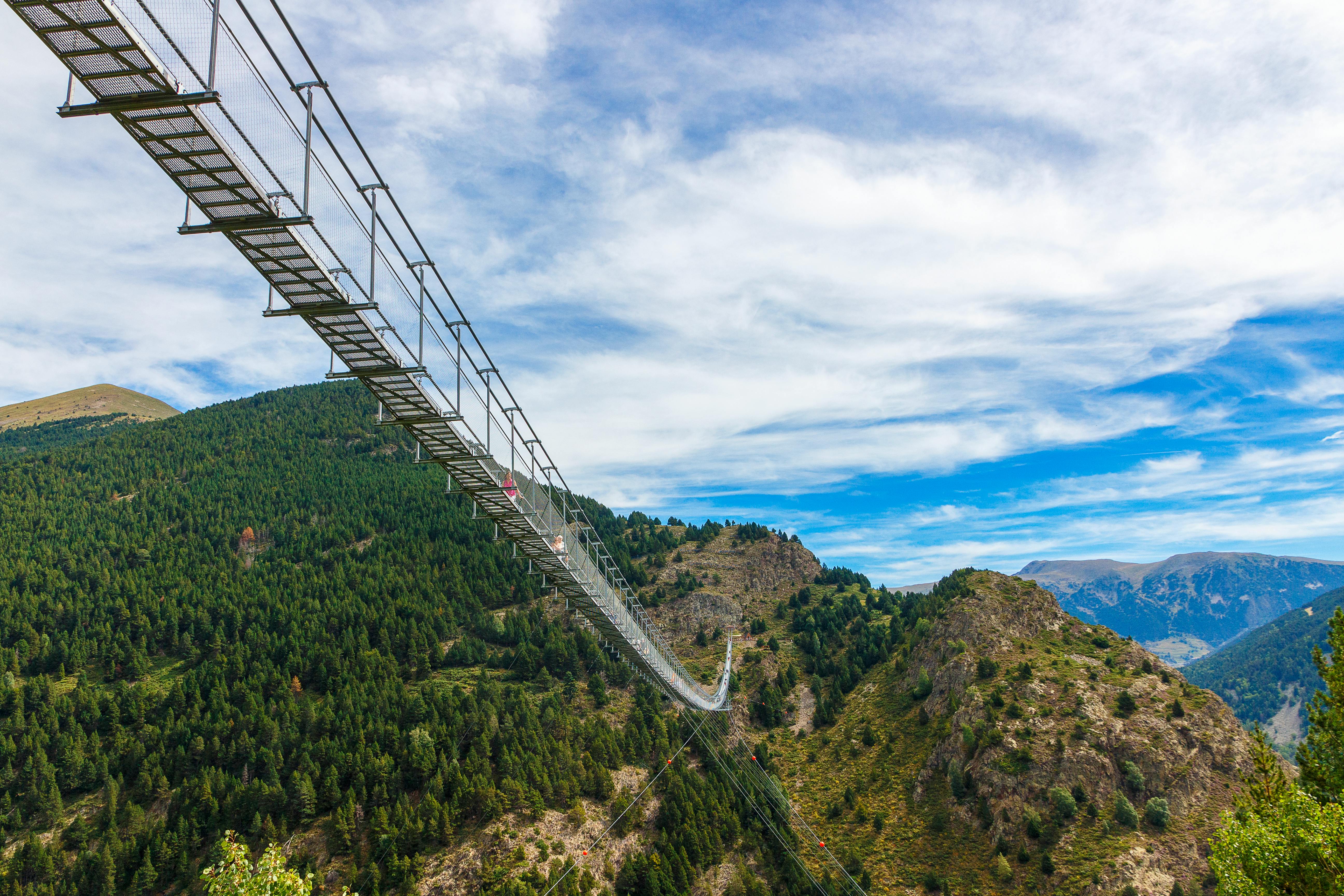 A suspension bridge over a valley with mountains in the background ...