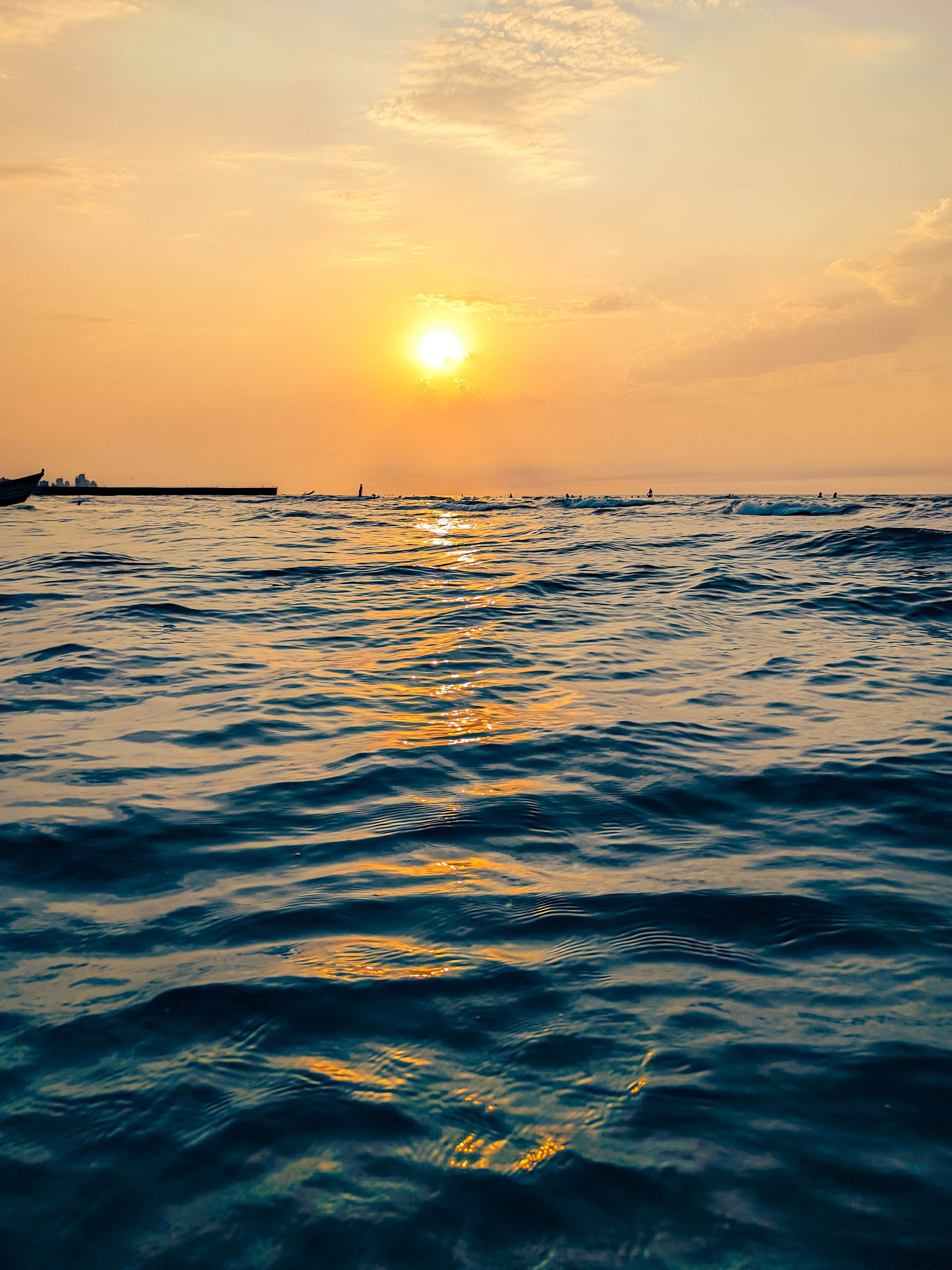 A sunset over the ocean with a boat in the water · Free Stock Photo