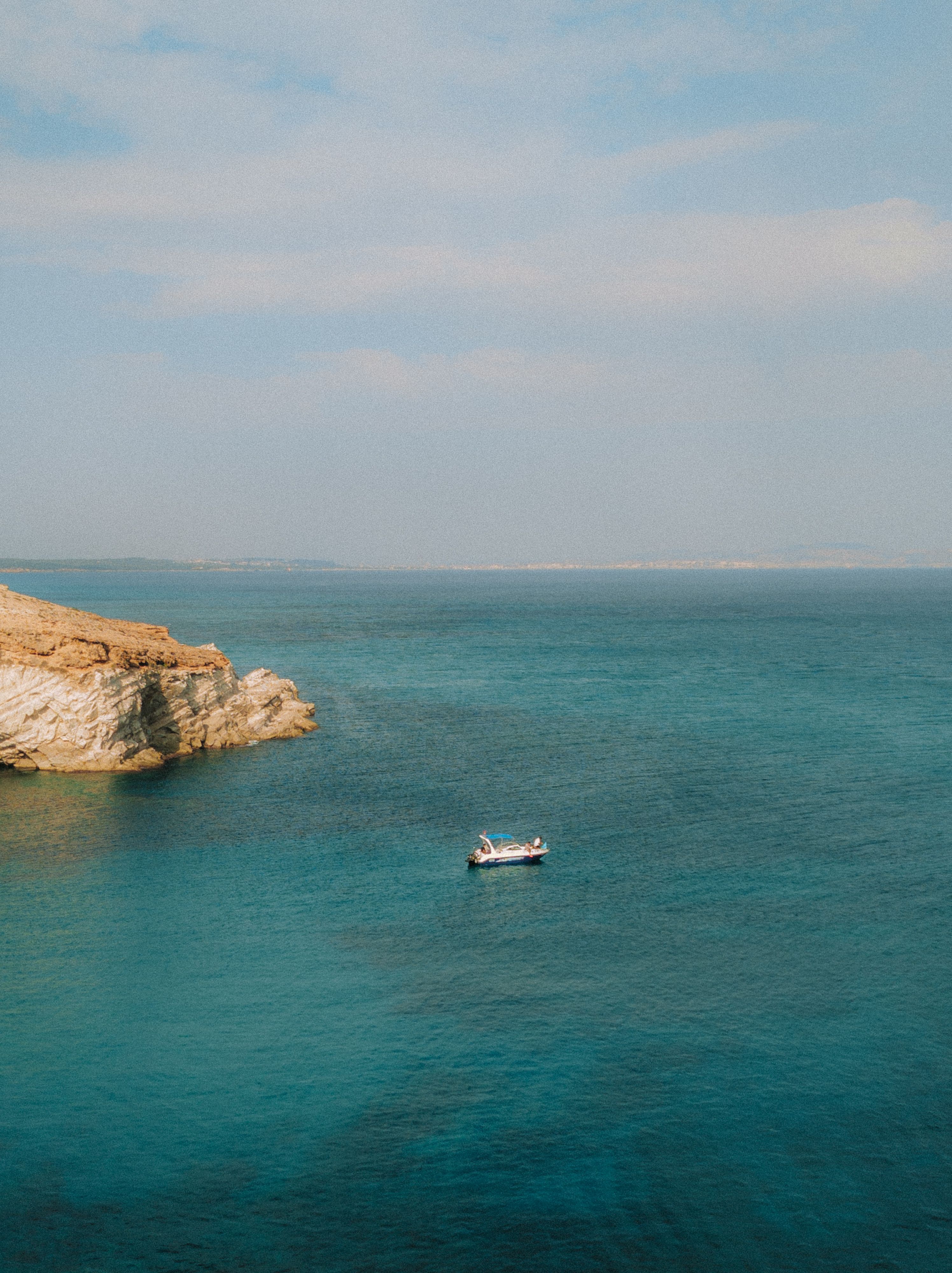 A boat is floating in the ocean near a cliff · Free Stock Photo