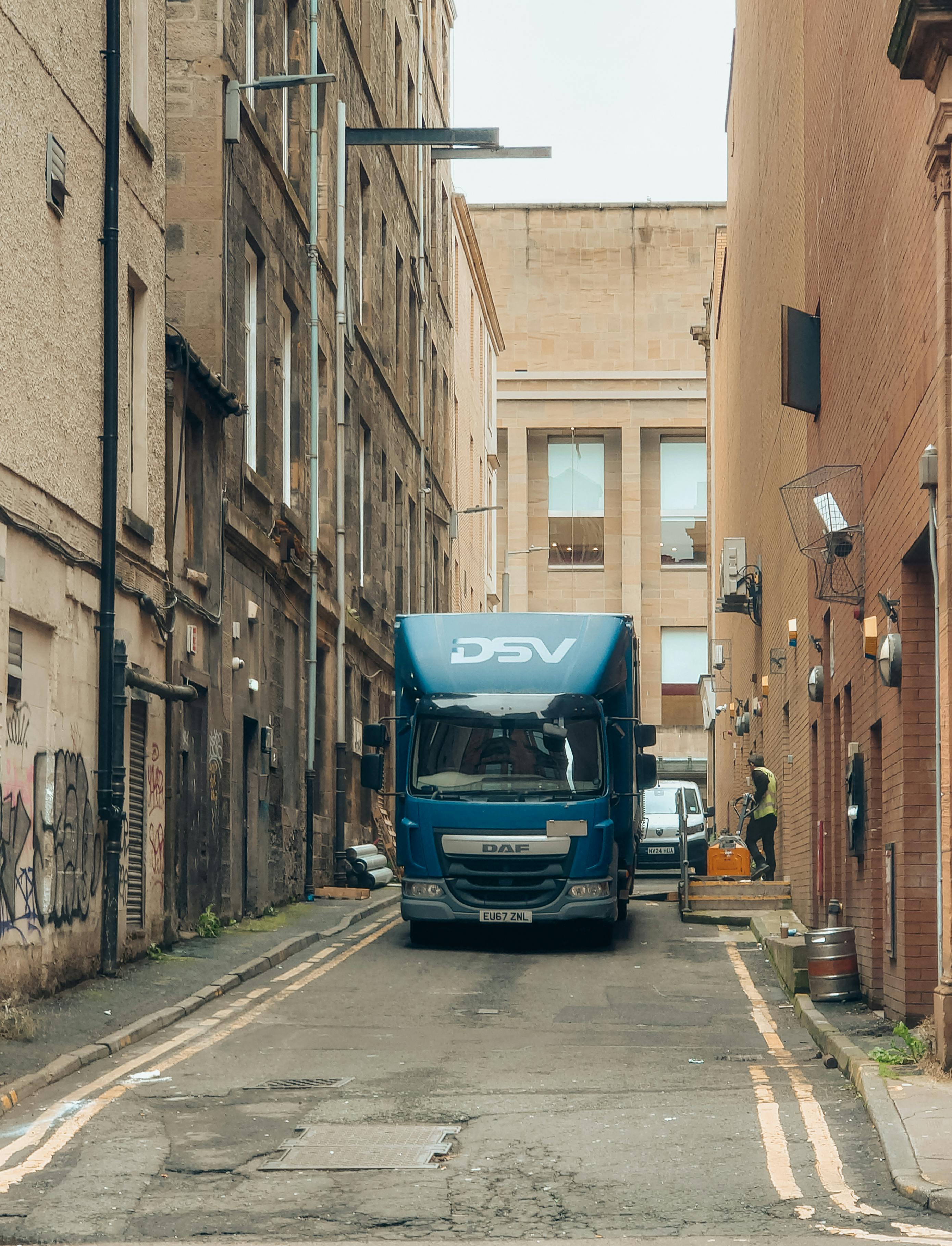 A blue truck driving down a narrow alley · Free Stock Photo
