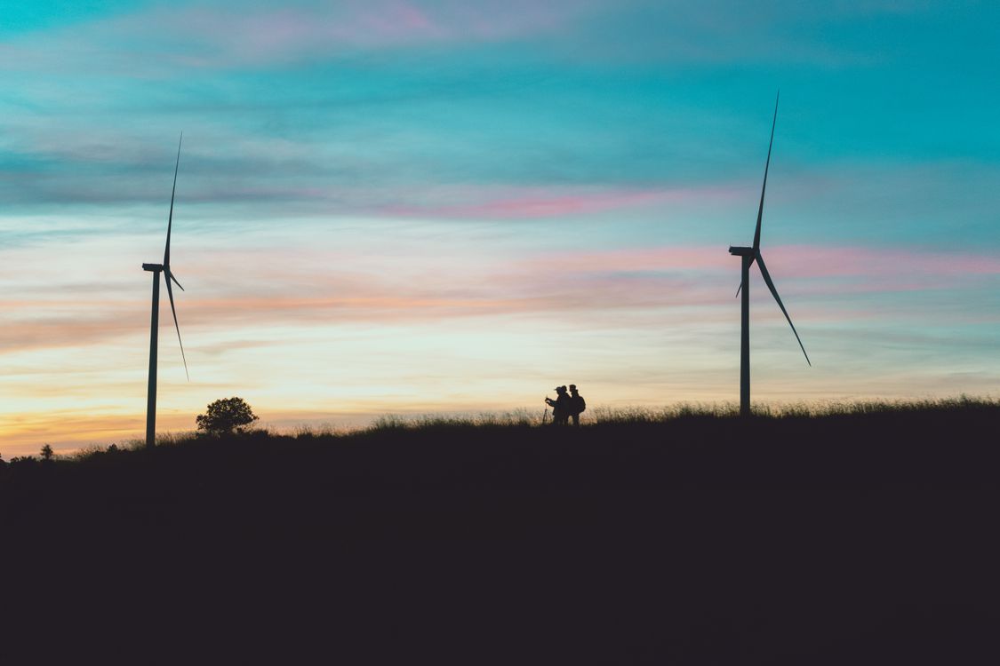 Silhouette of two people on a hill with wind turbines in the background ...