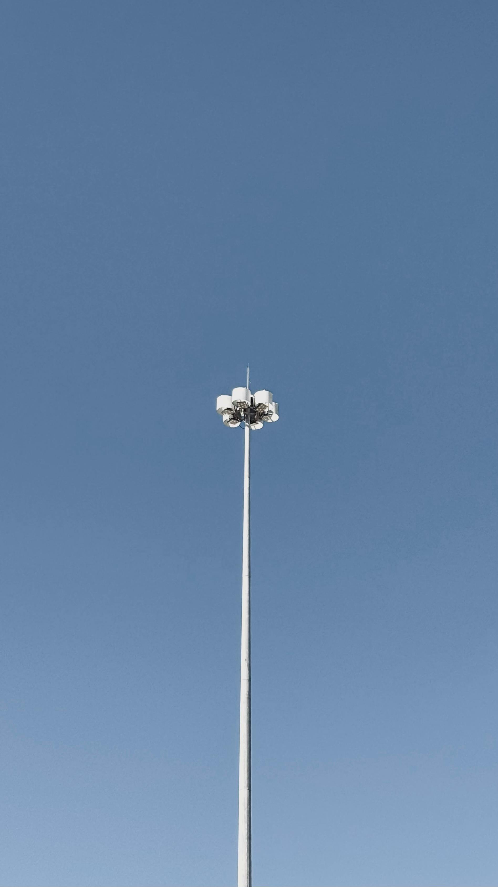 A tall light pole with a blue sky in the background · Free Stock Photo