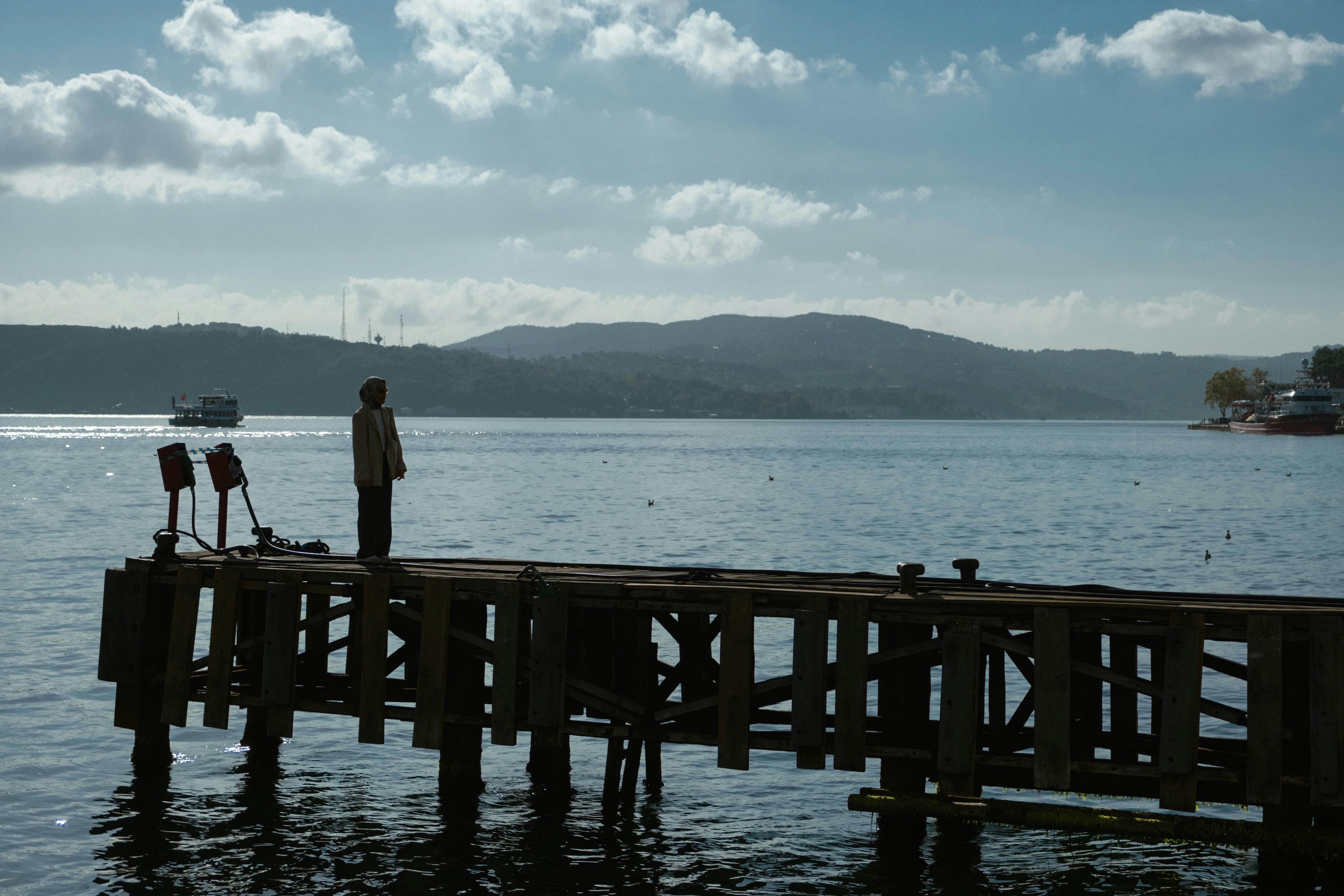 A man standing on a dock looking out over the water · Free Stock Photo