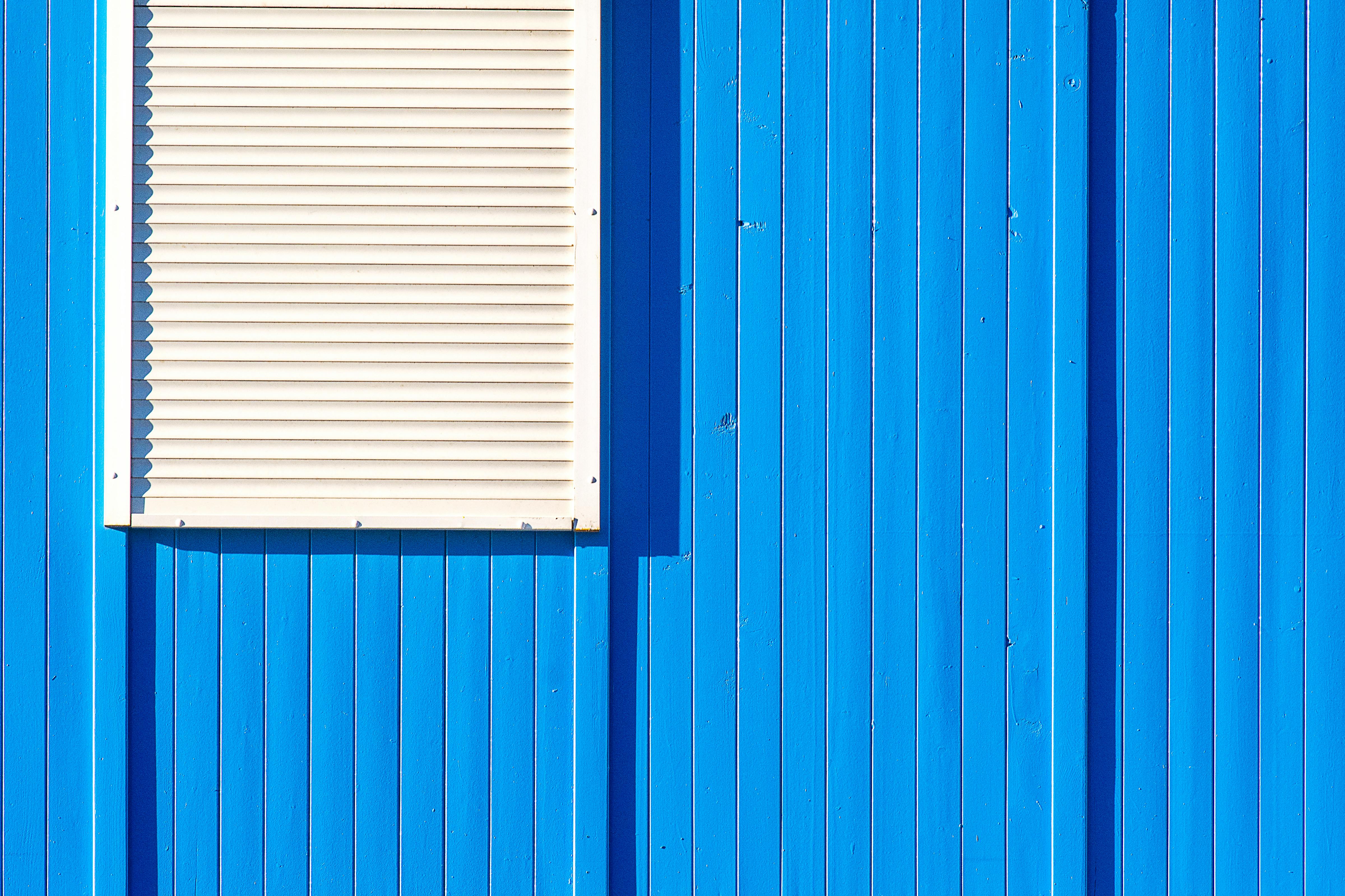 A blue metal building with a window and shutter · Free Stock Photo