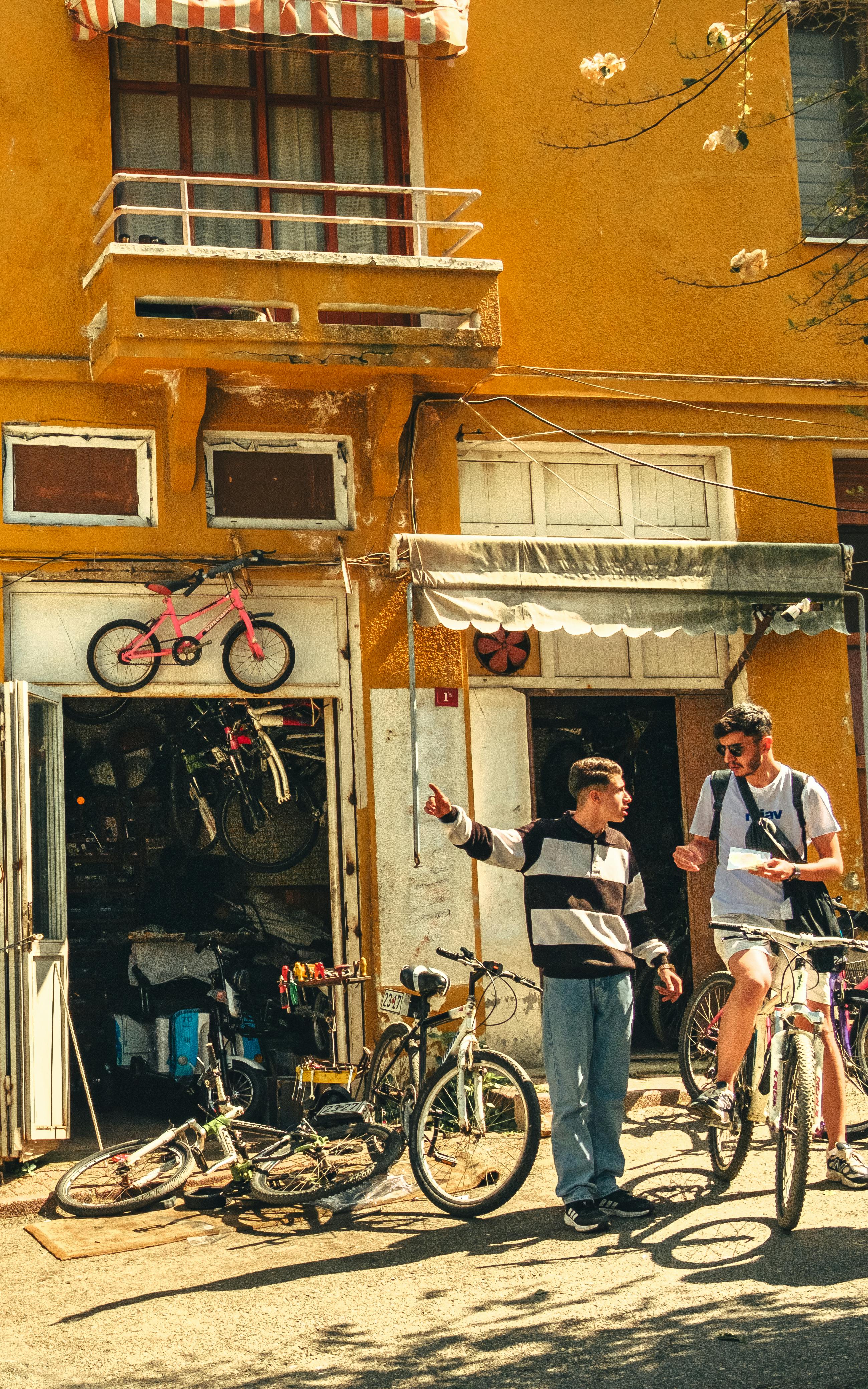 Two people standing outside of a yellow building with bicycles · Free ...