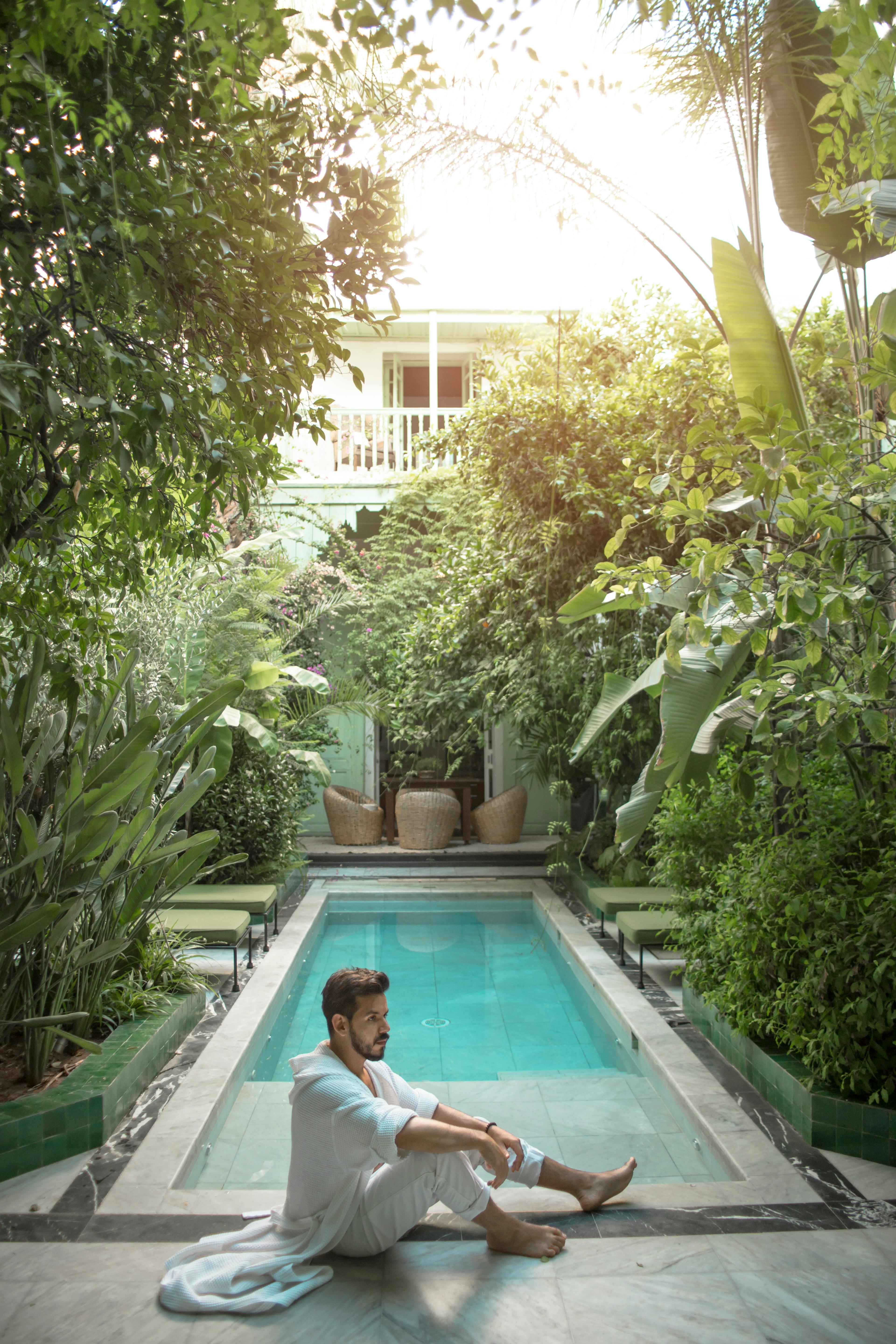 Man Sitting Near at Pool Side surrounded by Plants · Free Stock Photo