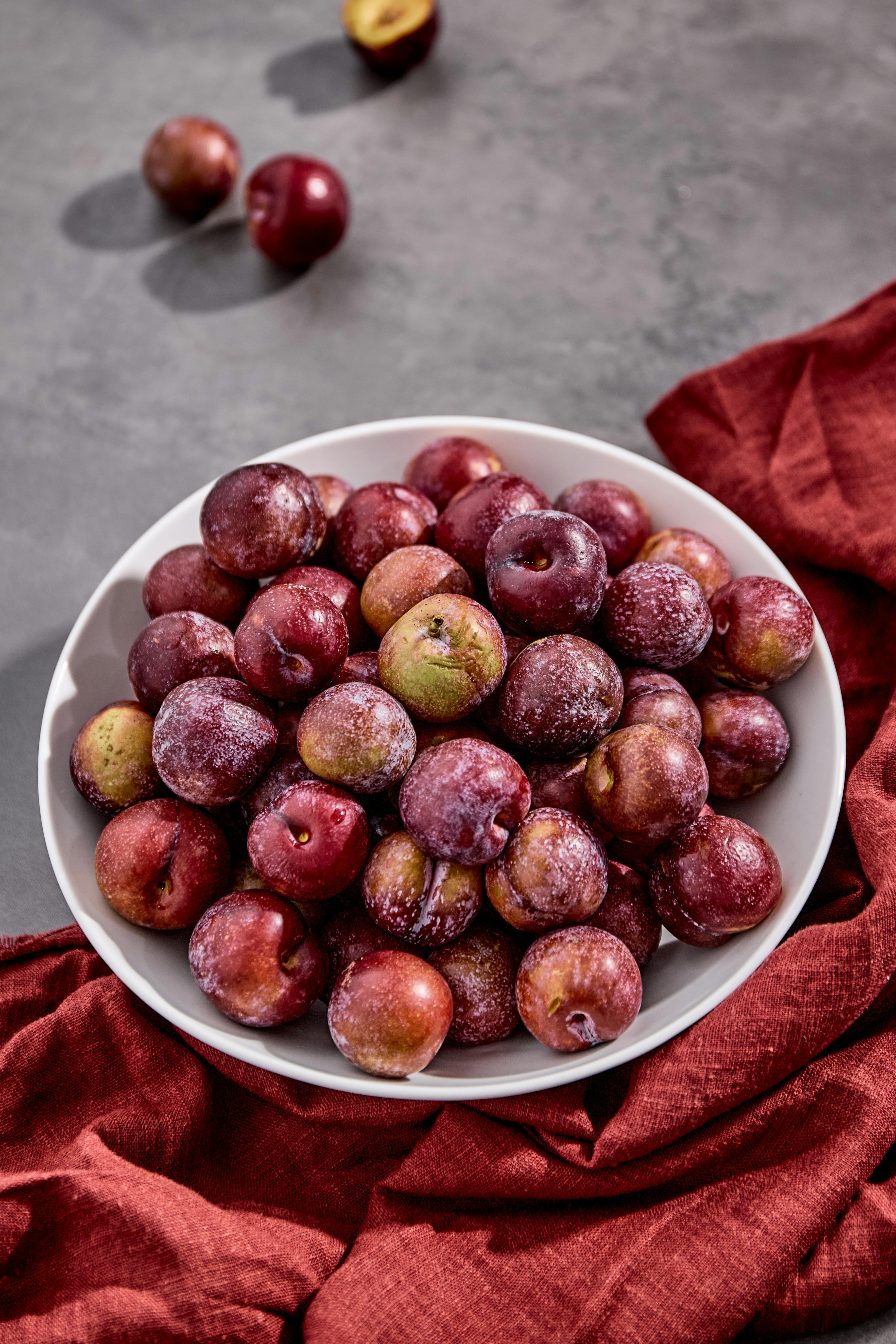 A bowl of plums on a table with red cloth · Free Stock Photo