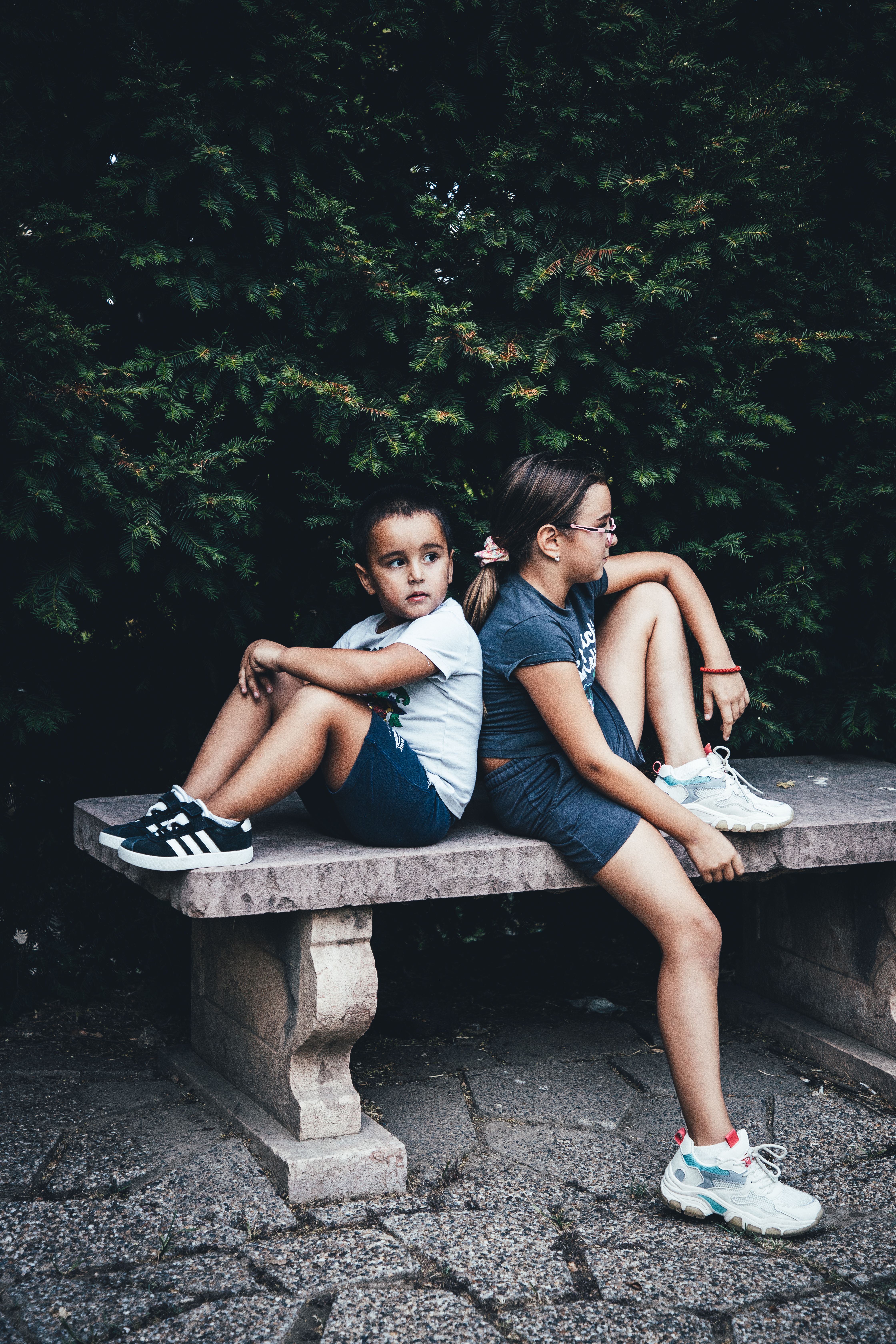 Two children sitting on a bench in front of a tree · Free Stock Photo