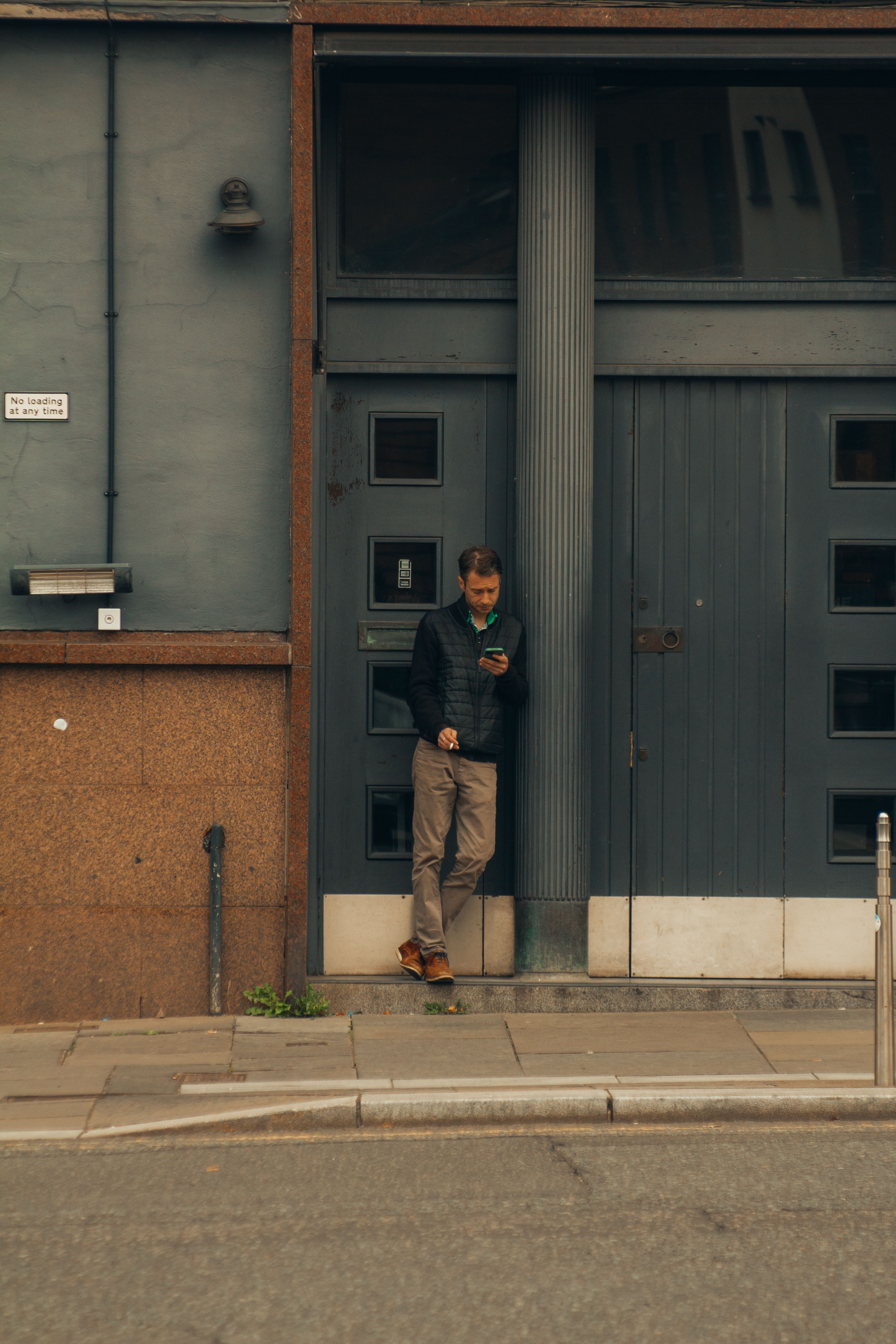 Man Leaning on a Column with a Smartphone in Hand · Free Stock Photo