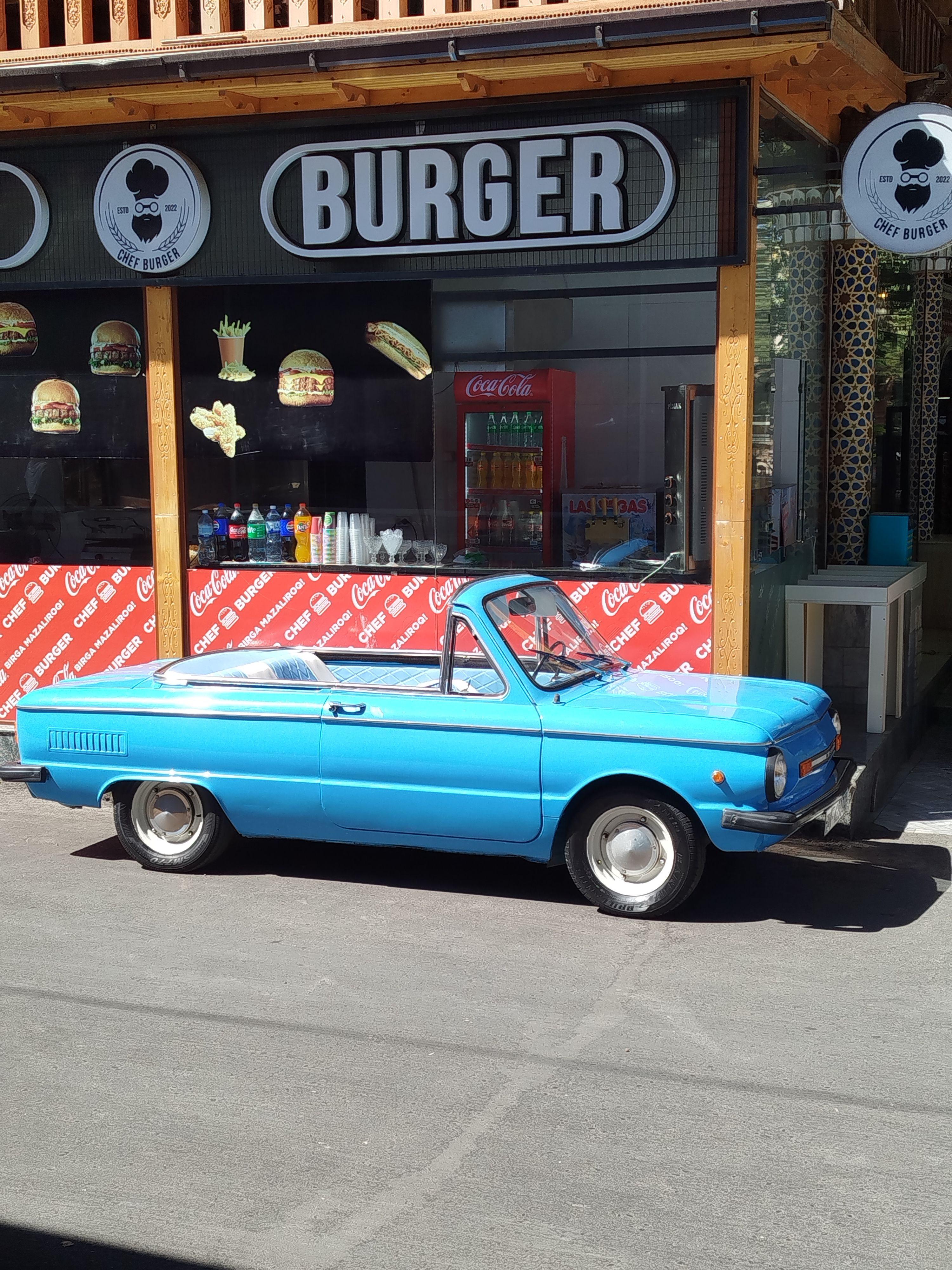 A small blue car parked in front of a burger shop · Free Stock Photo