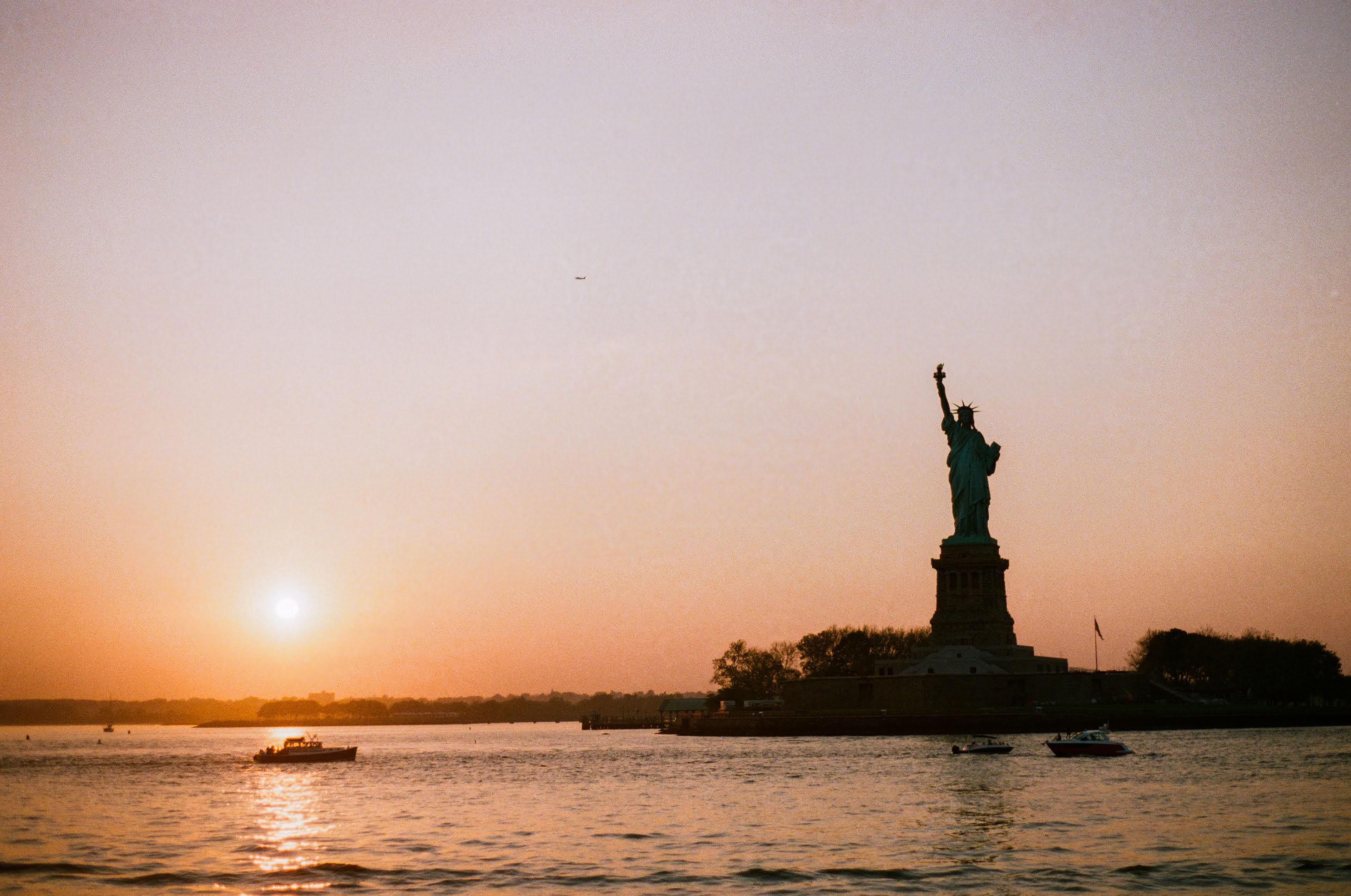 The statue of liberty is seen at sunset · Free Stock Photo