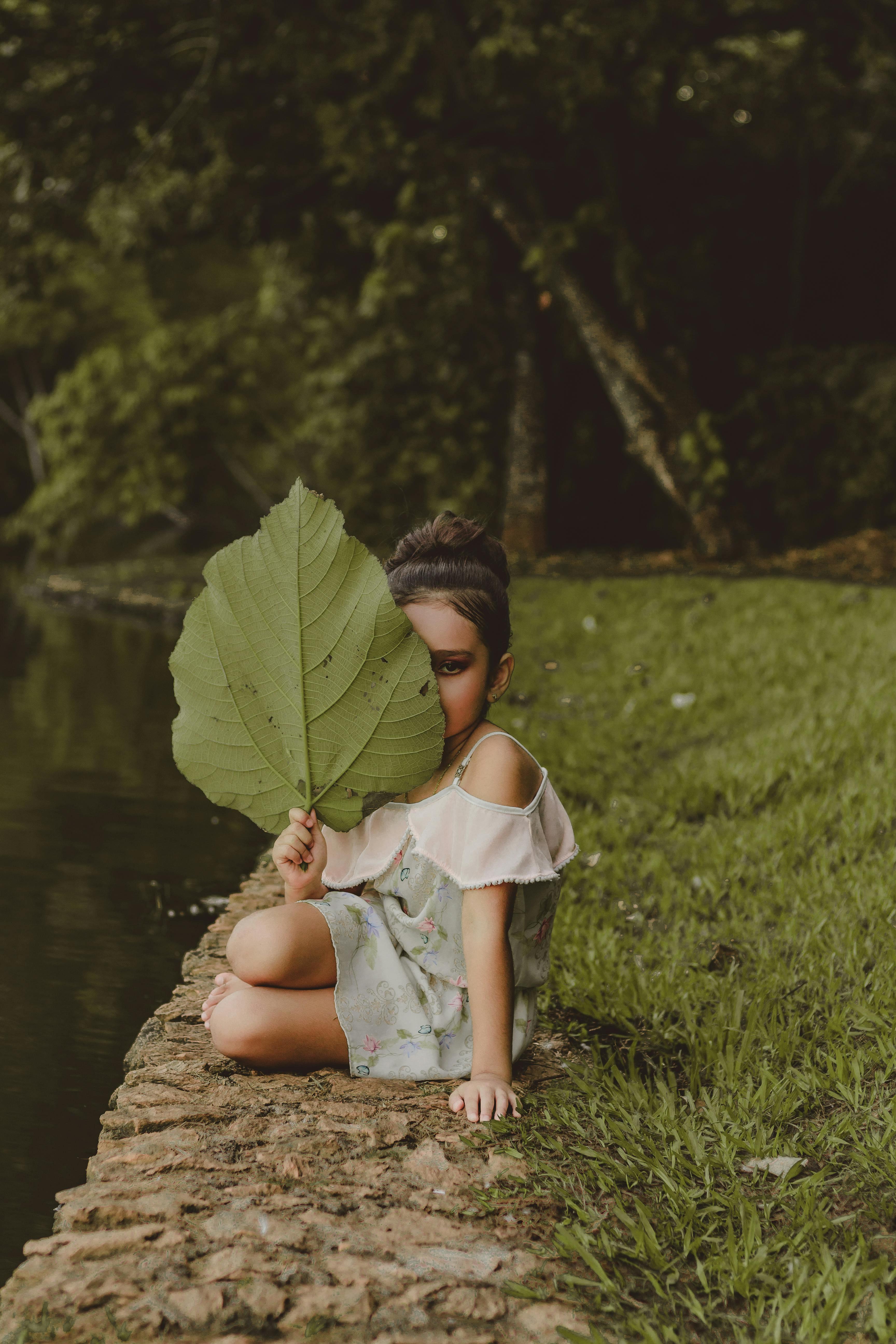 A Girl Sitting on the Ground While Covering Half of Her Face with a ...
