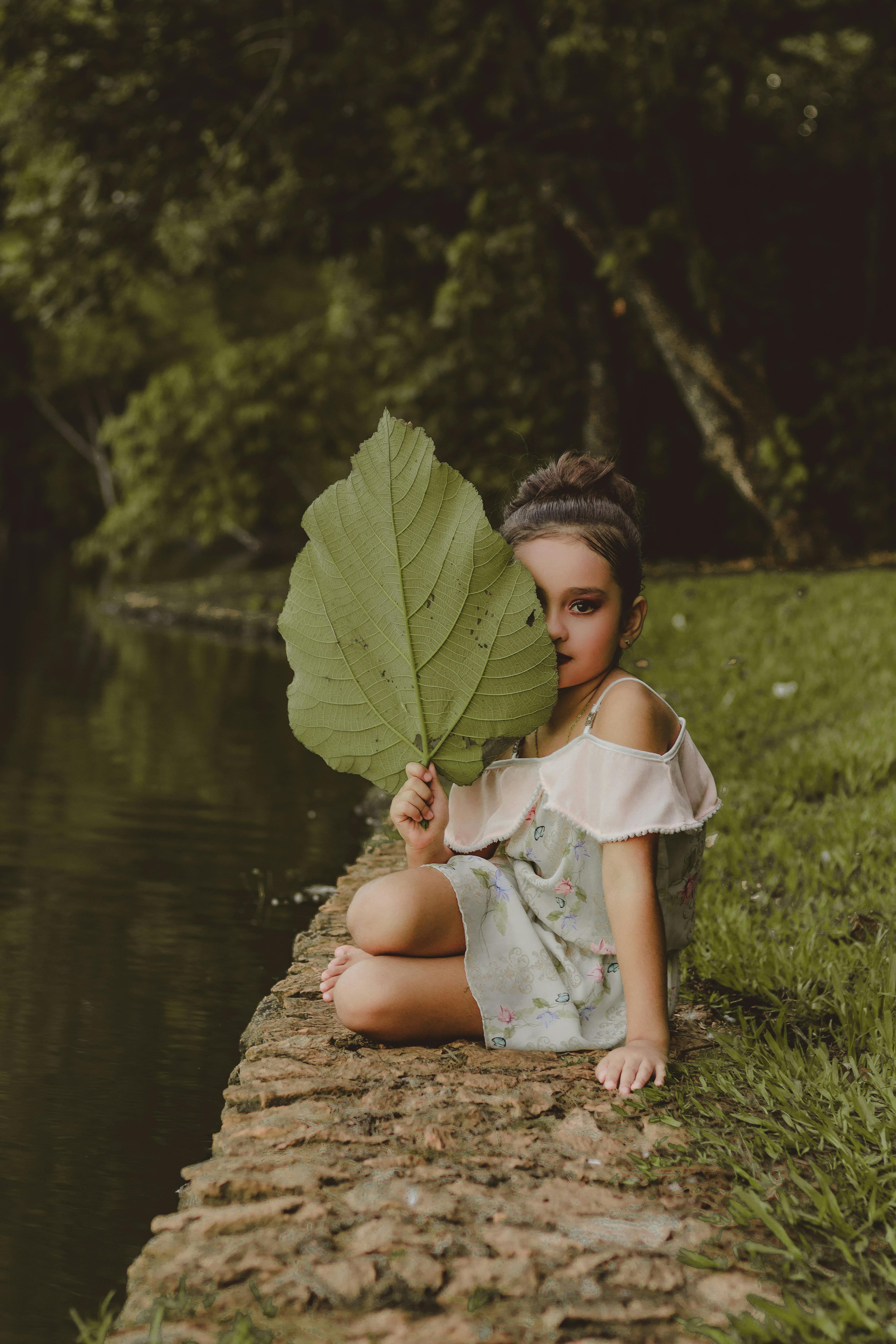 A Girl Sitting on the Ground While Covering Half of Her Face with a ...