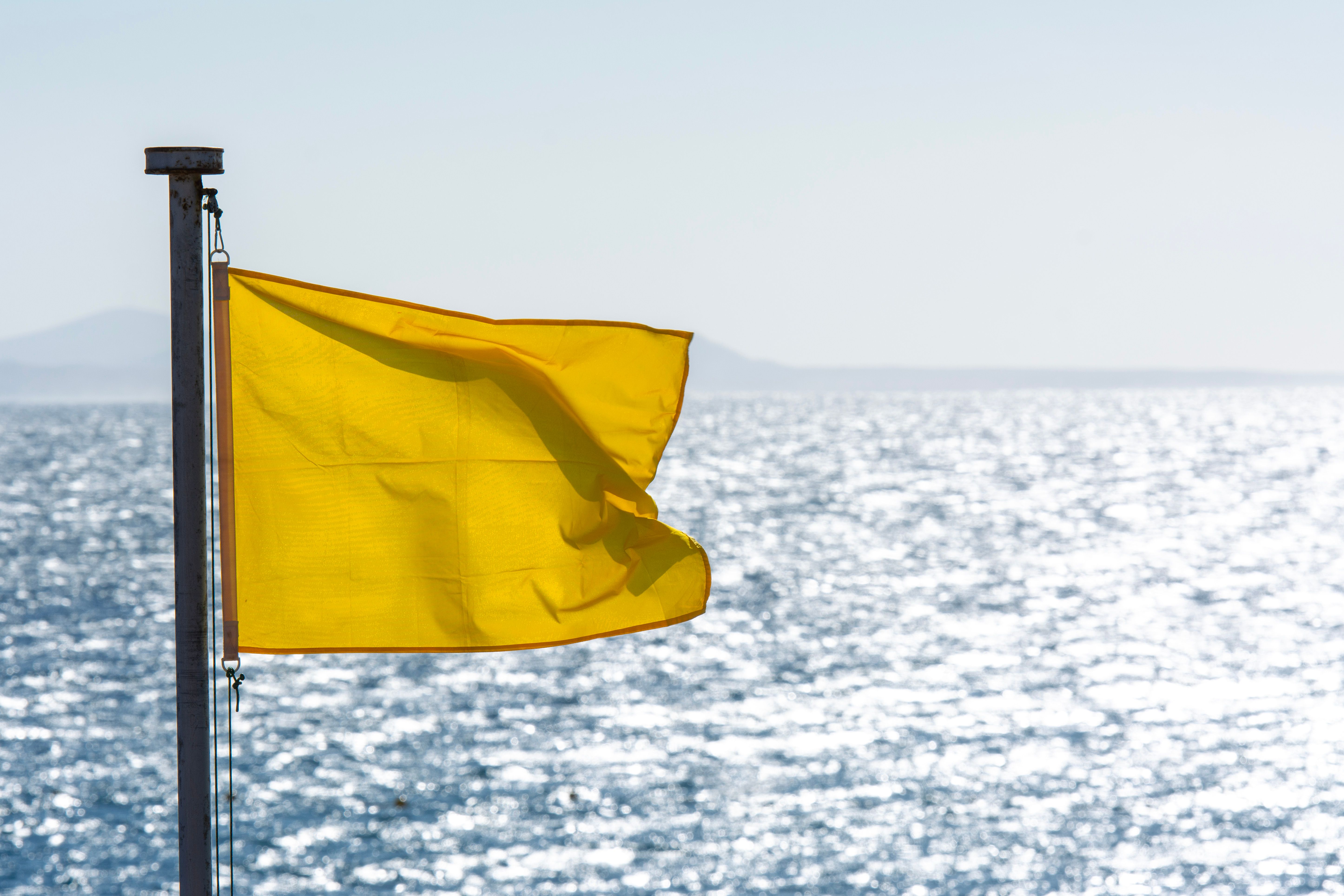 Yellow Flag Fluttering against the Sea · Free Stock Photo