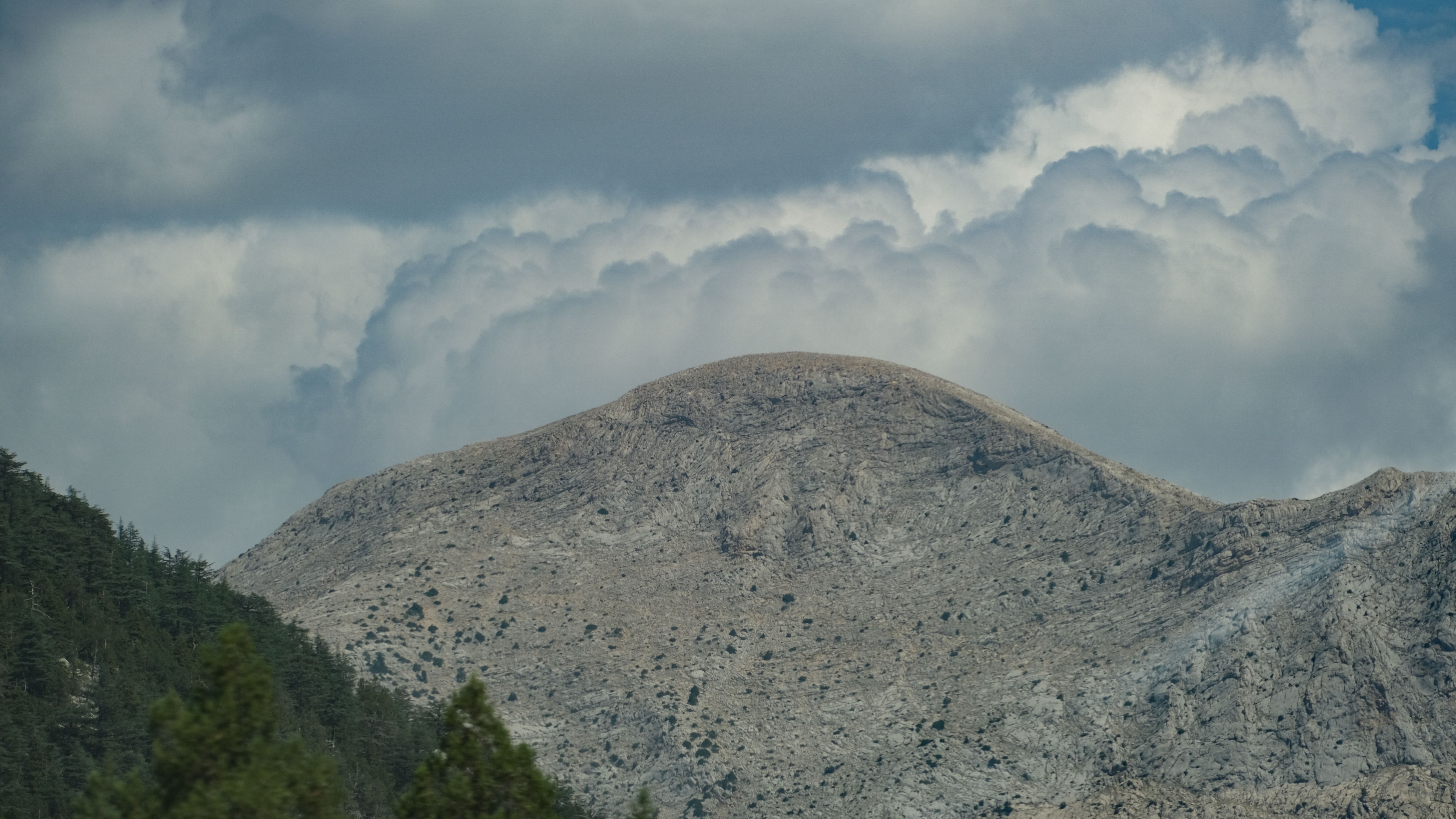 A mountain with clouds and trees in the background · Free Stock Photo