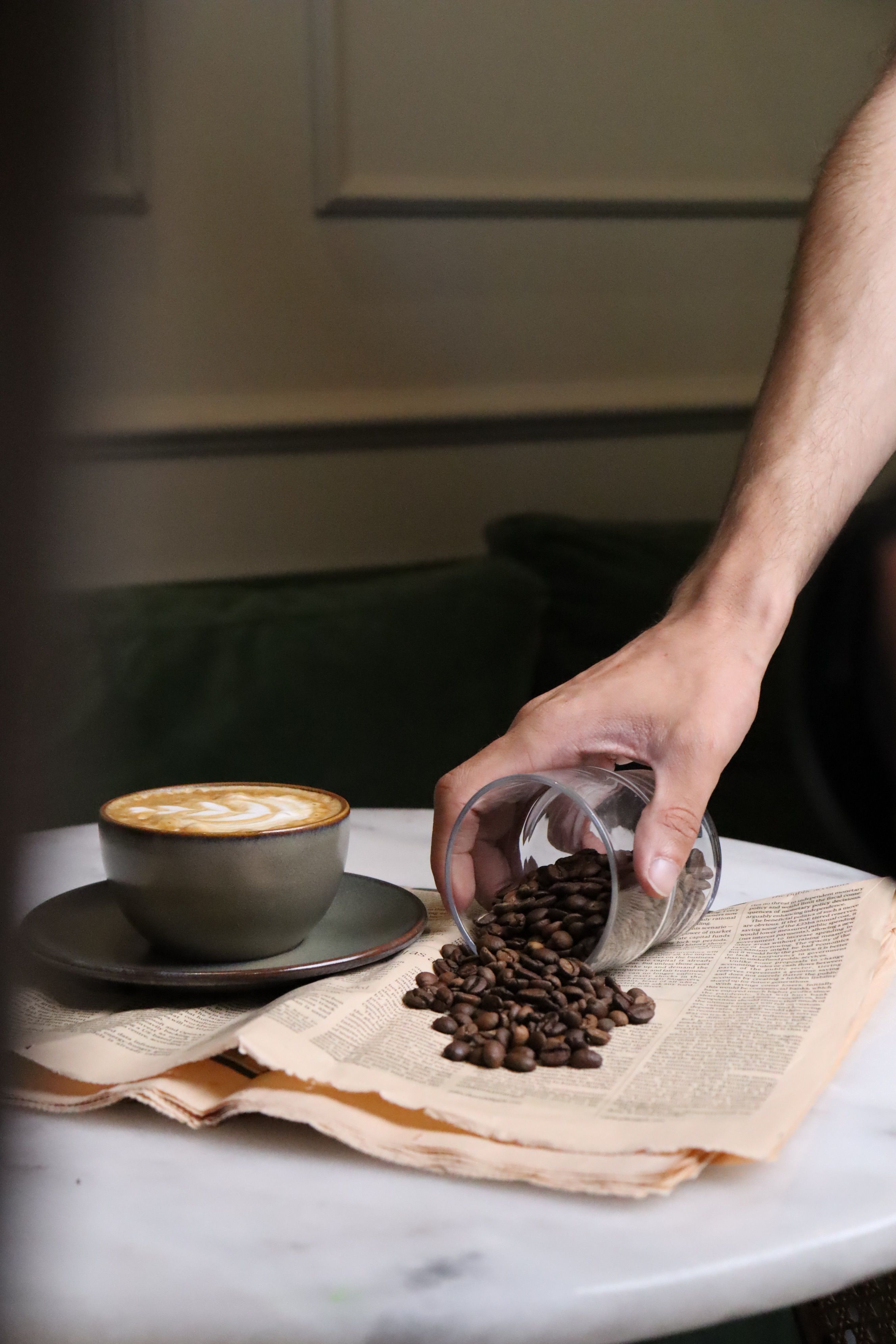 Hand Pouring Coffee Beans beside Cappuccino · Free Stock Photo