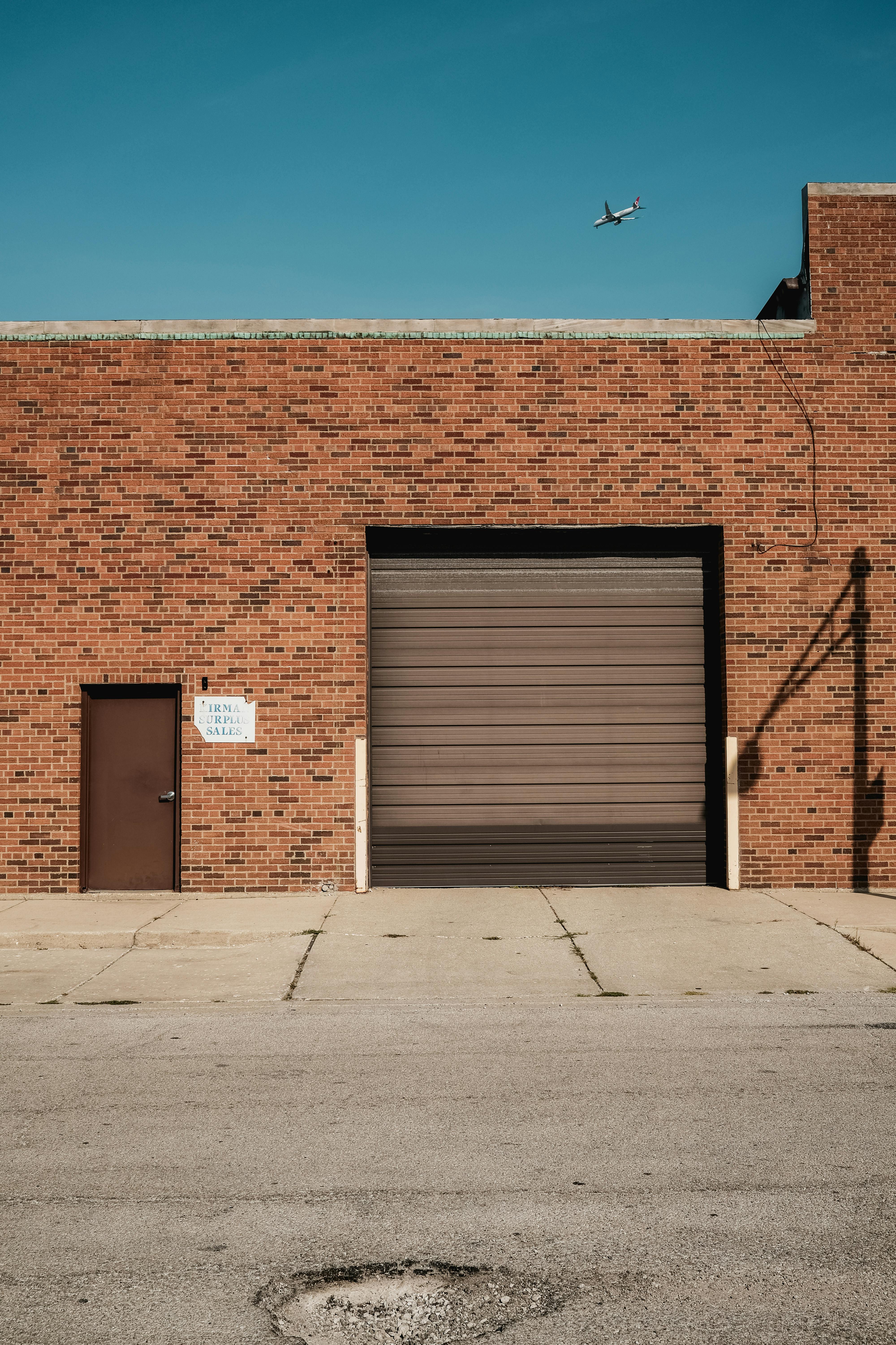 Industrial Brick Building with Airplane Overhead · Free Stock Photo