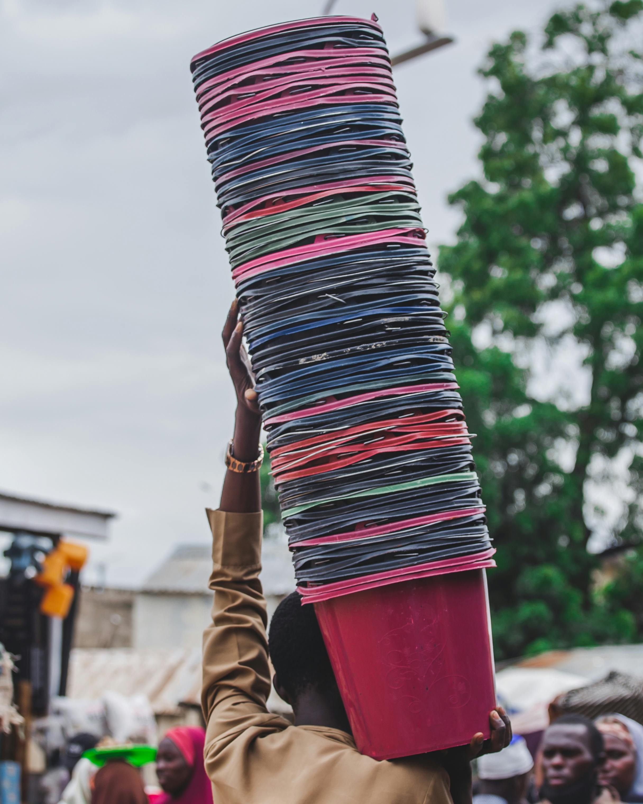 Person Carrying Tall Stack of Colorful Bins Outdoors · Free Stock Photo