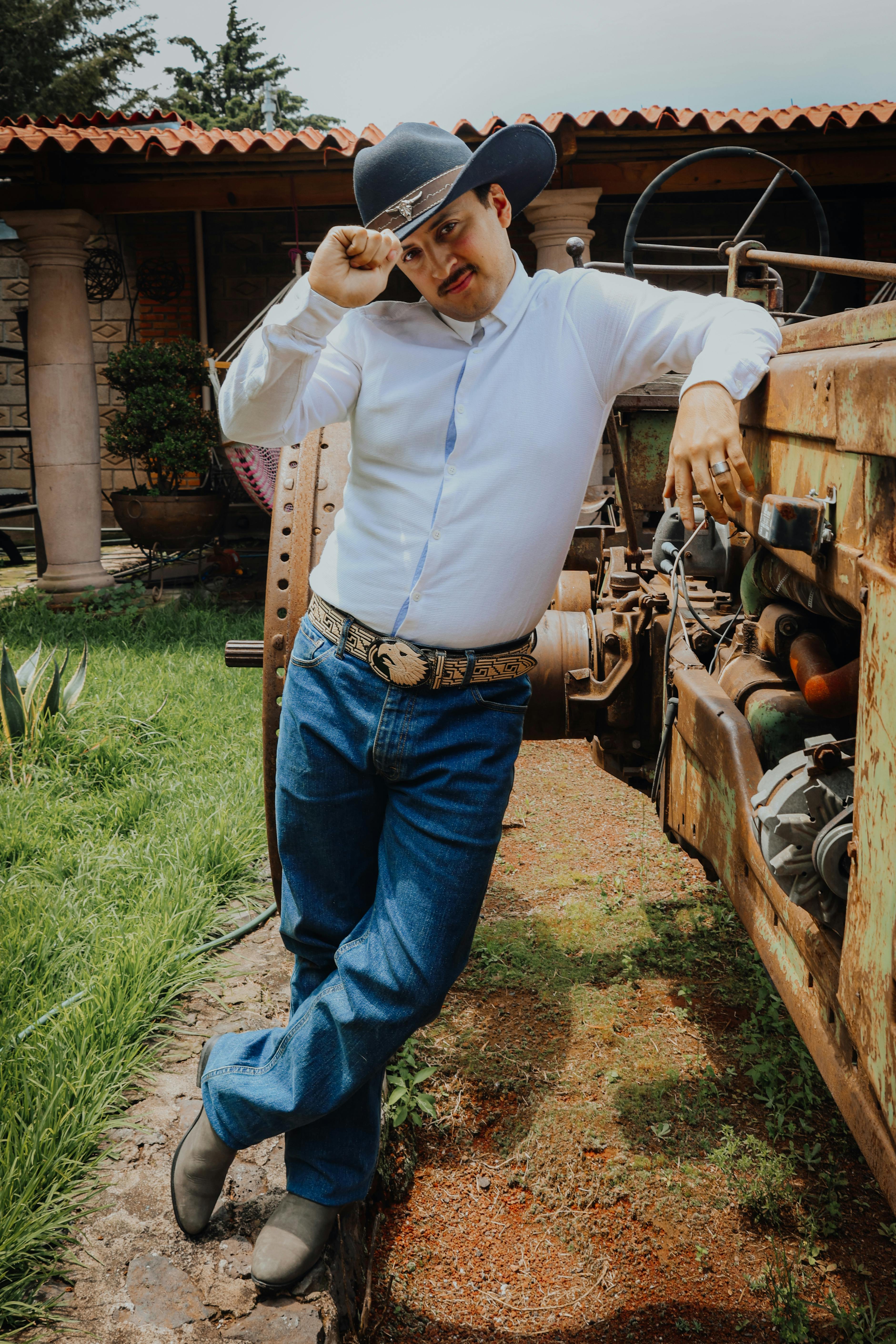 Cowboy Leaning on Rustic Tractor Outdoors · Free Stock Photo