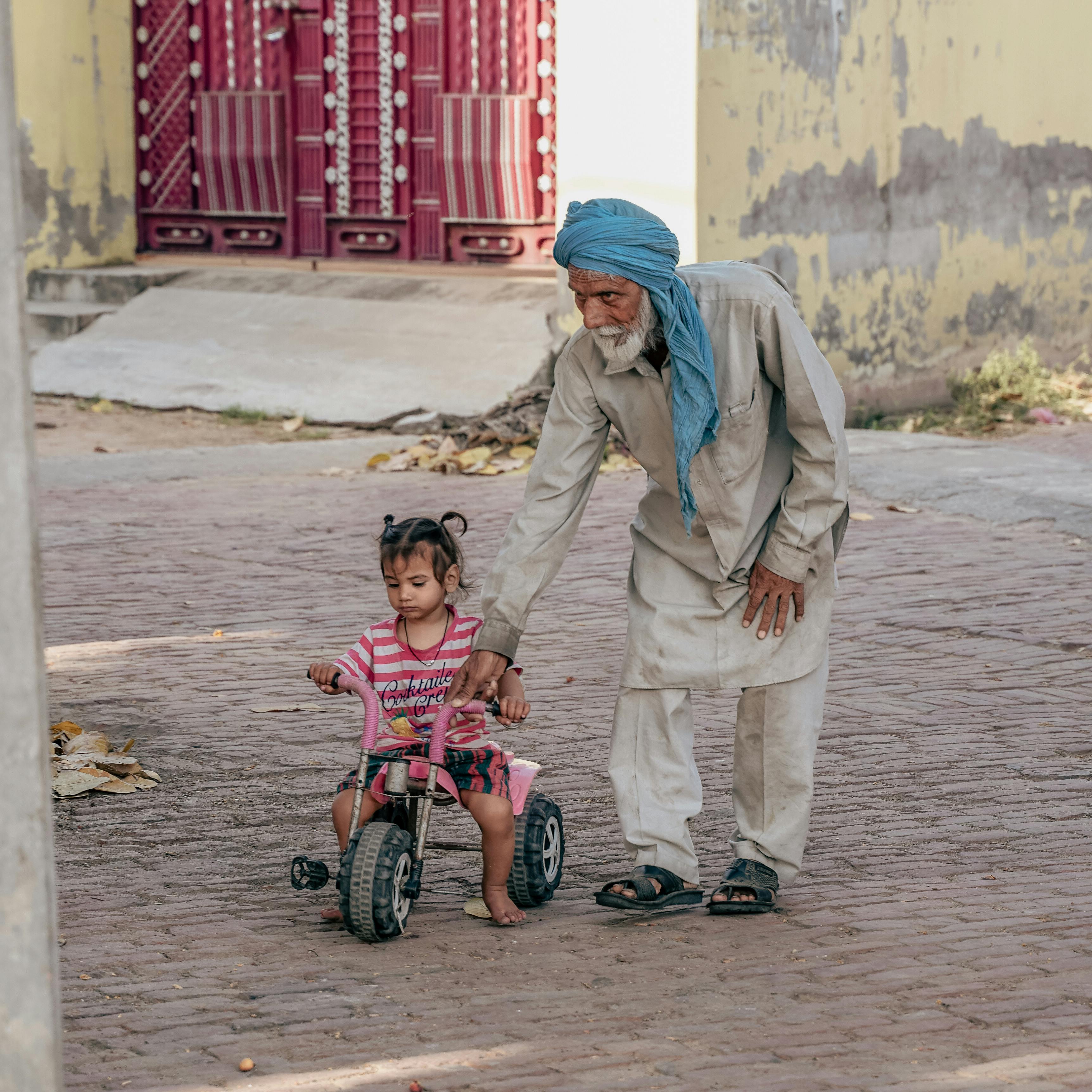 Grandfather guiding child on tricycle outdoors · Free Stock Photo