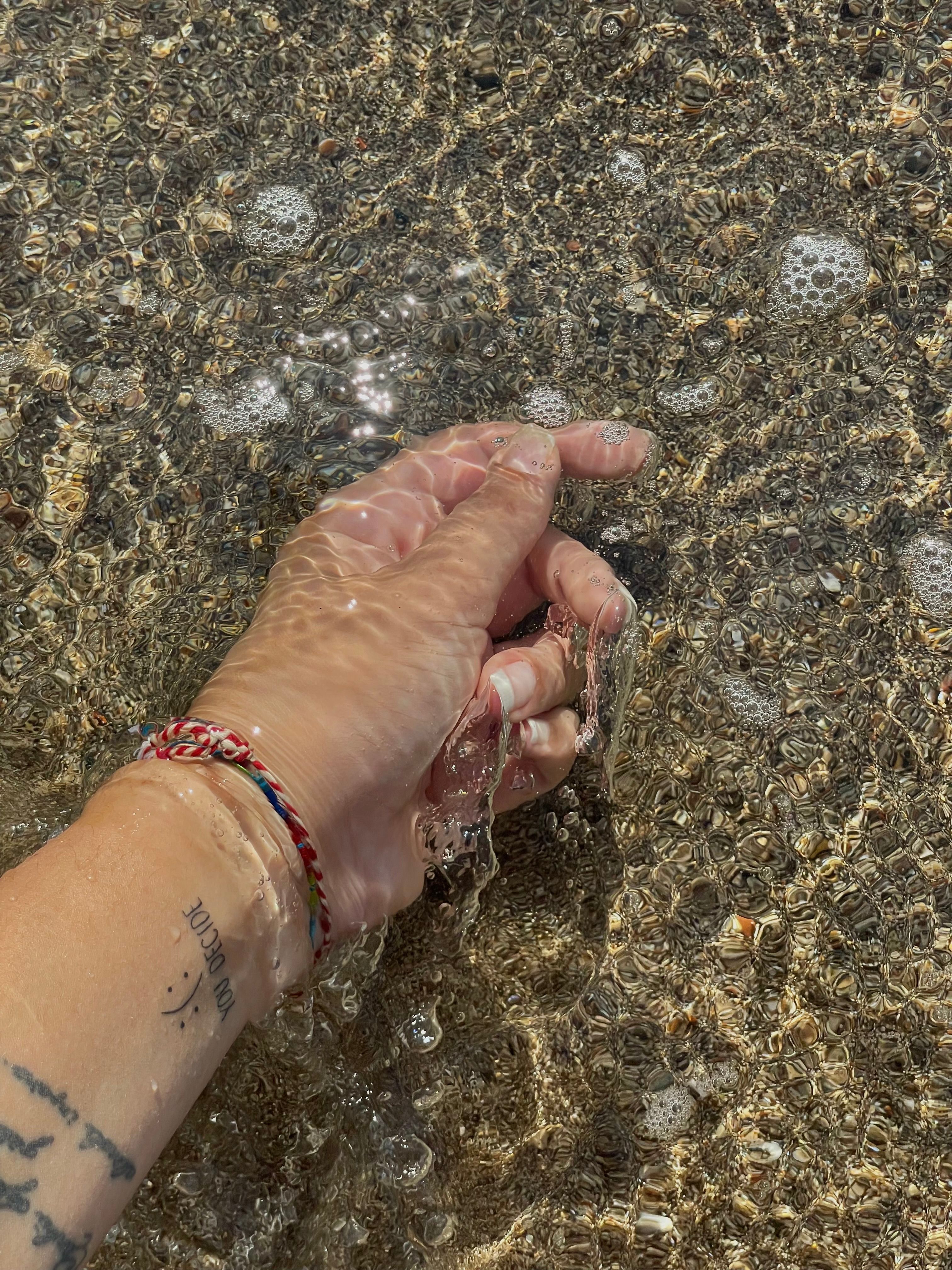 Hand in Clear Ocean Water on Rocky Shoreline · Free Stock Photo
