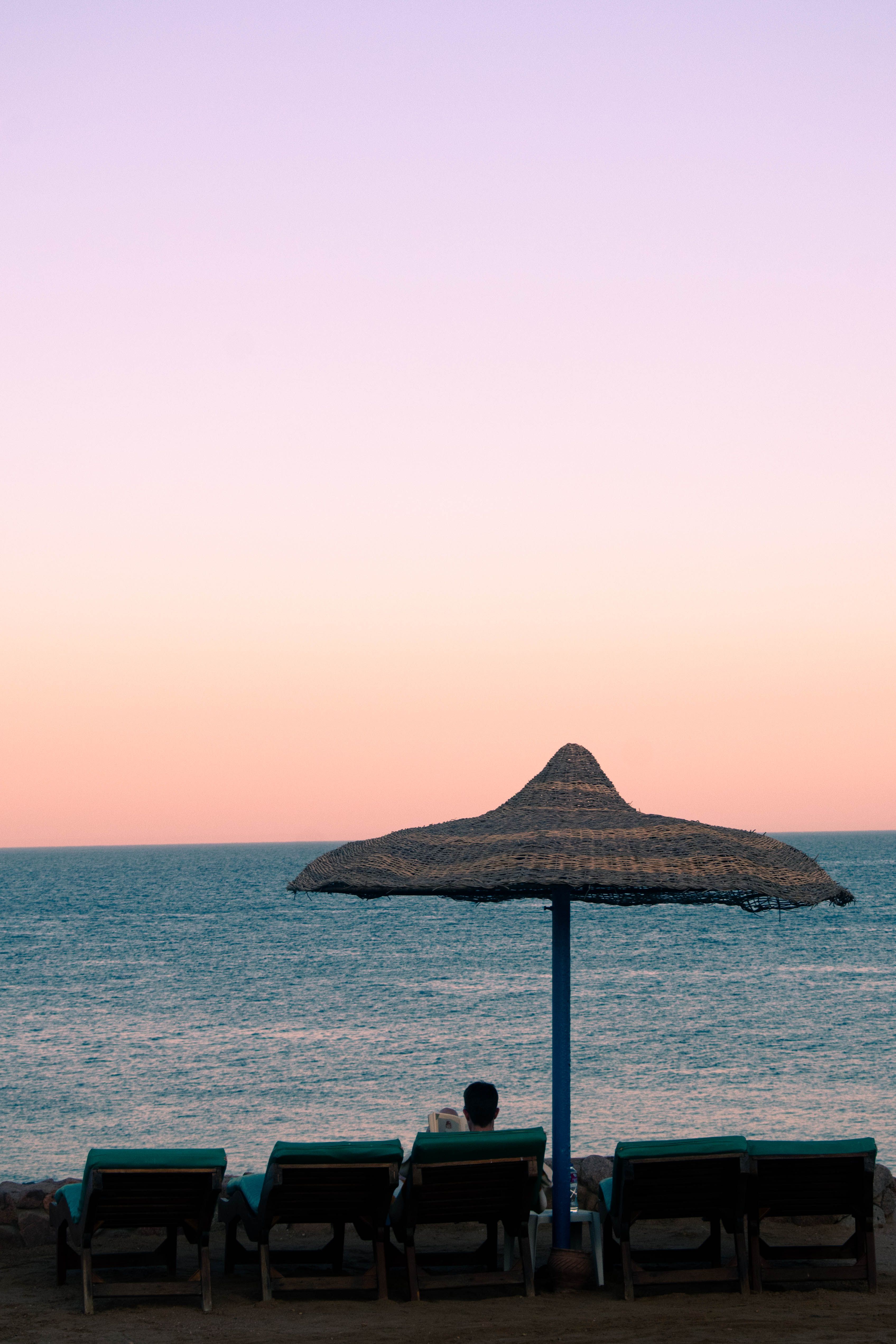 Tranquil Beach Sunset with Straw Umbrella · Free Stock Photo