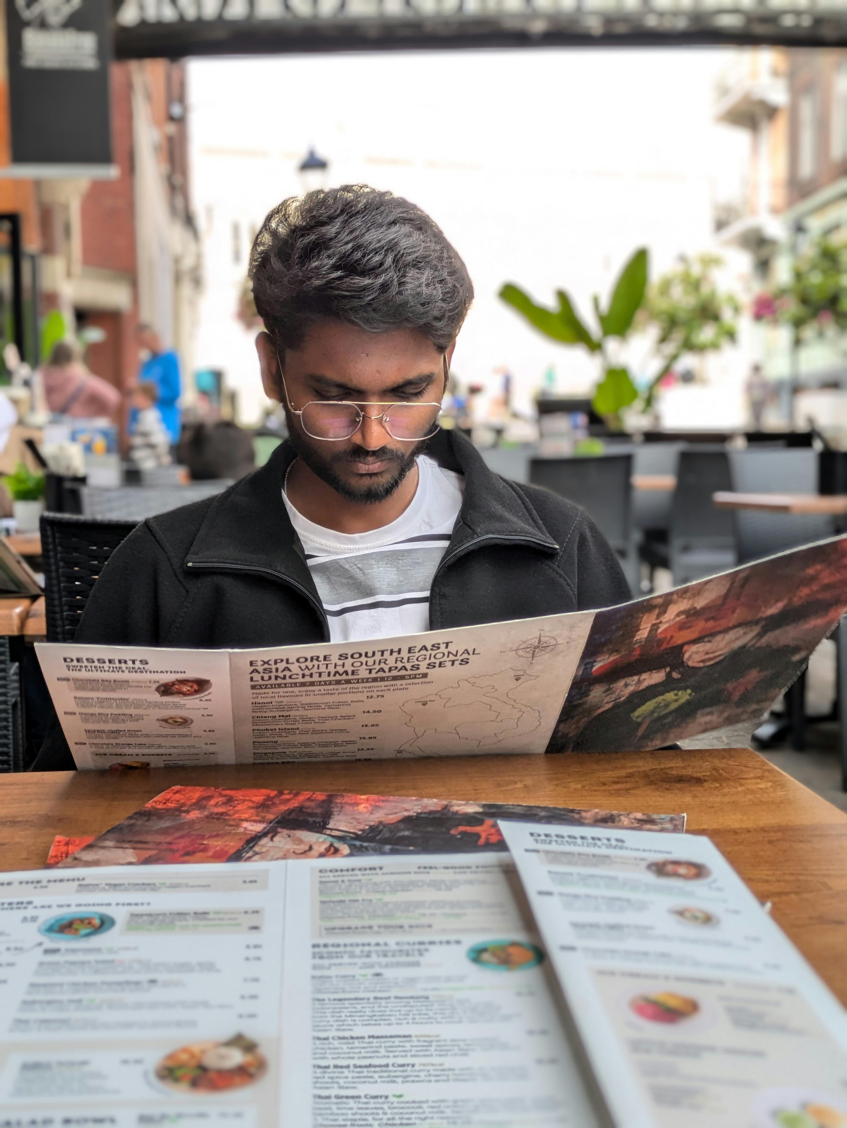 Young man reading menu at outdoor cafe table · Free Stock Photo