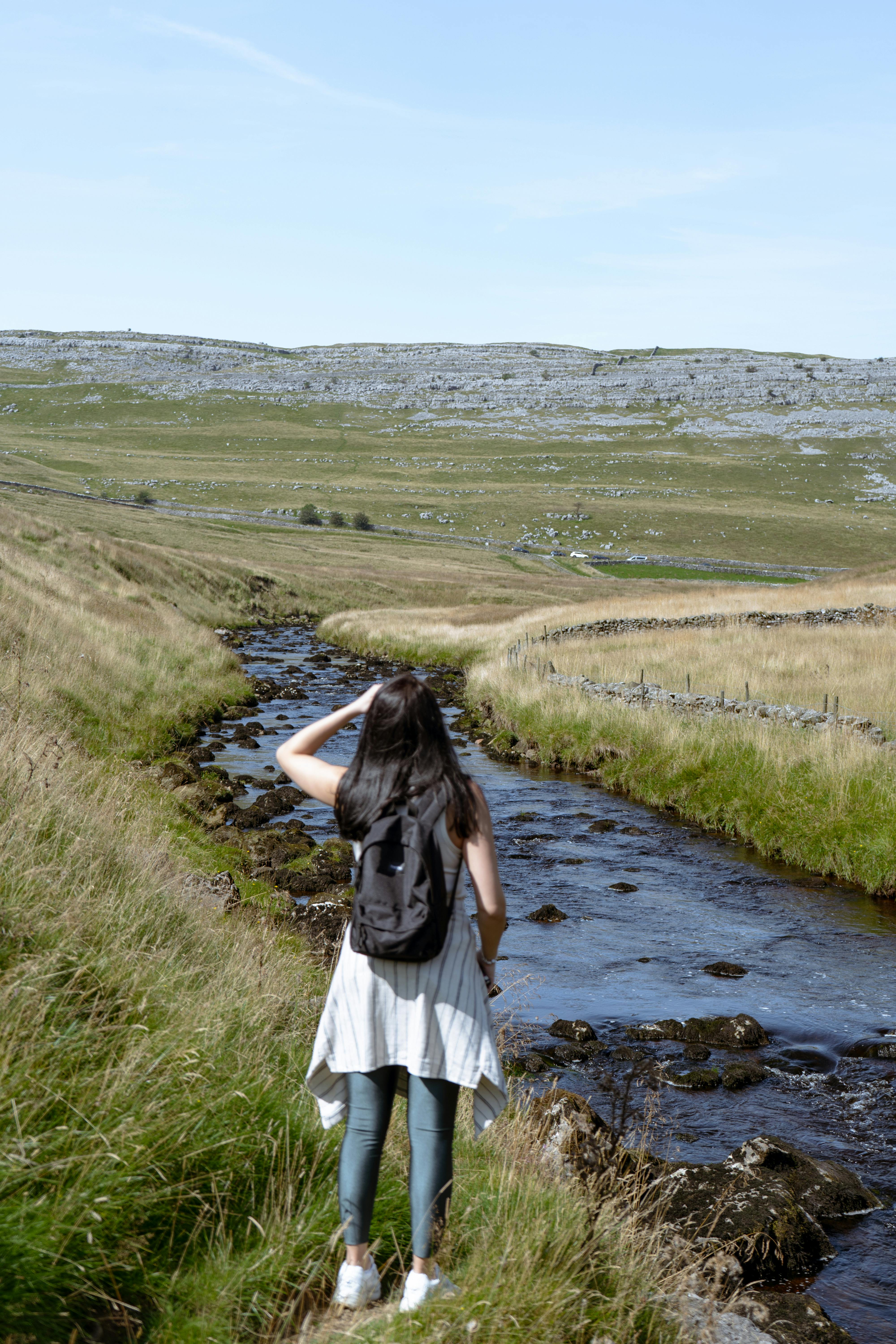 Woman Hiking Along Tranquil Stream in Countryside · Free Stock Photo