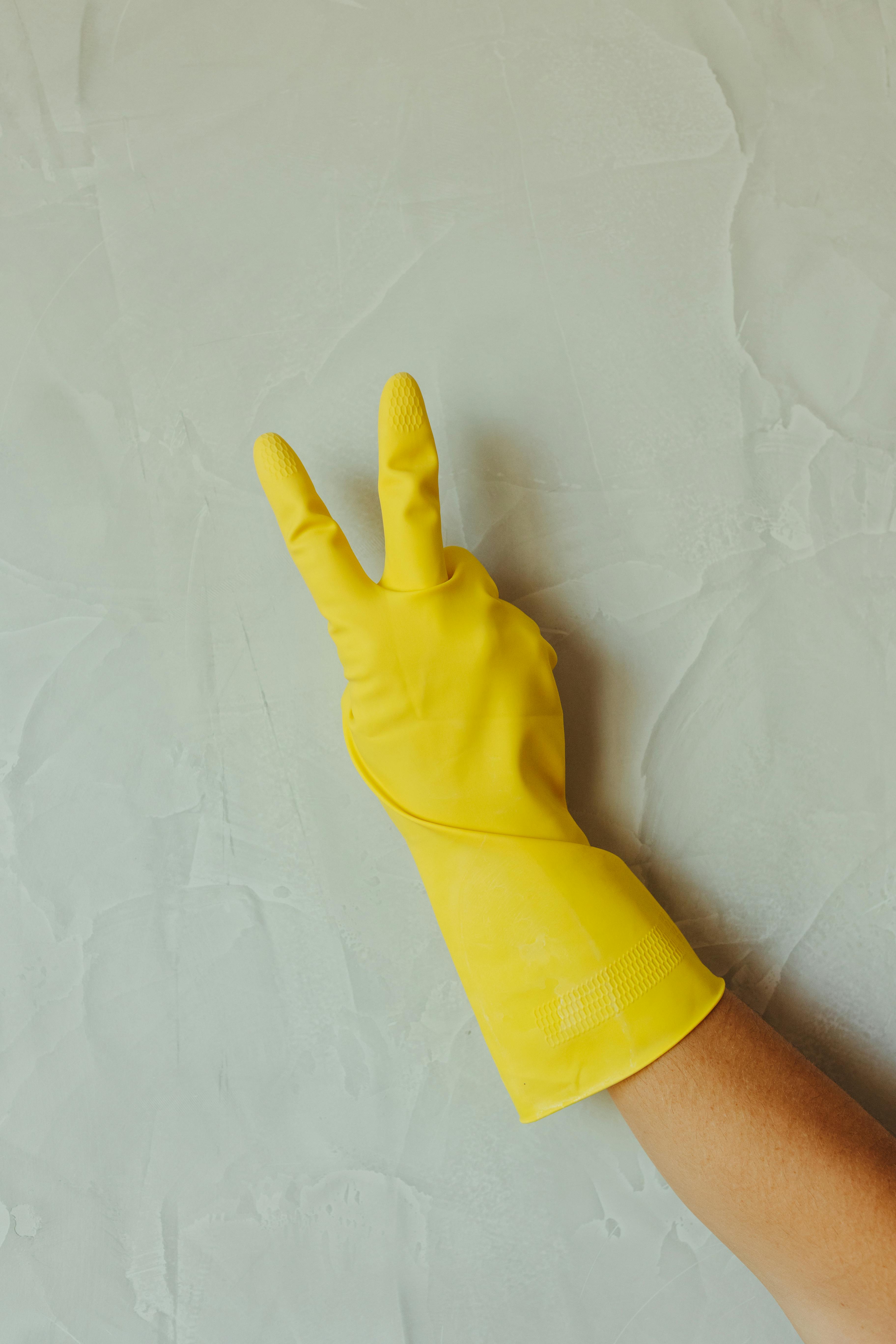 Yellow Gloved Hand Showing Peace Sign on Textured Wall · Free Stock Photo