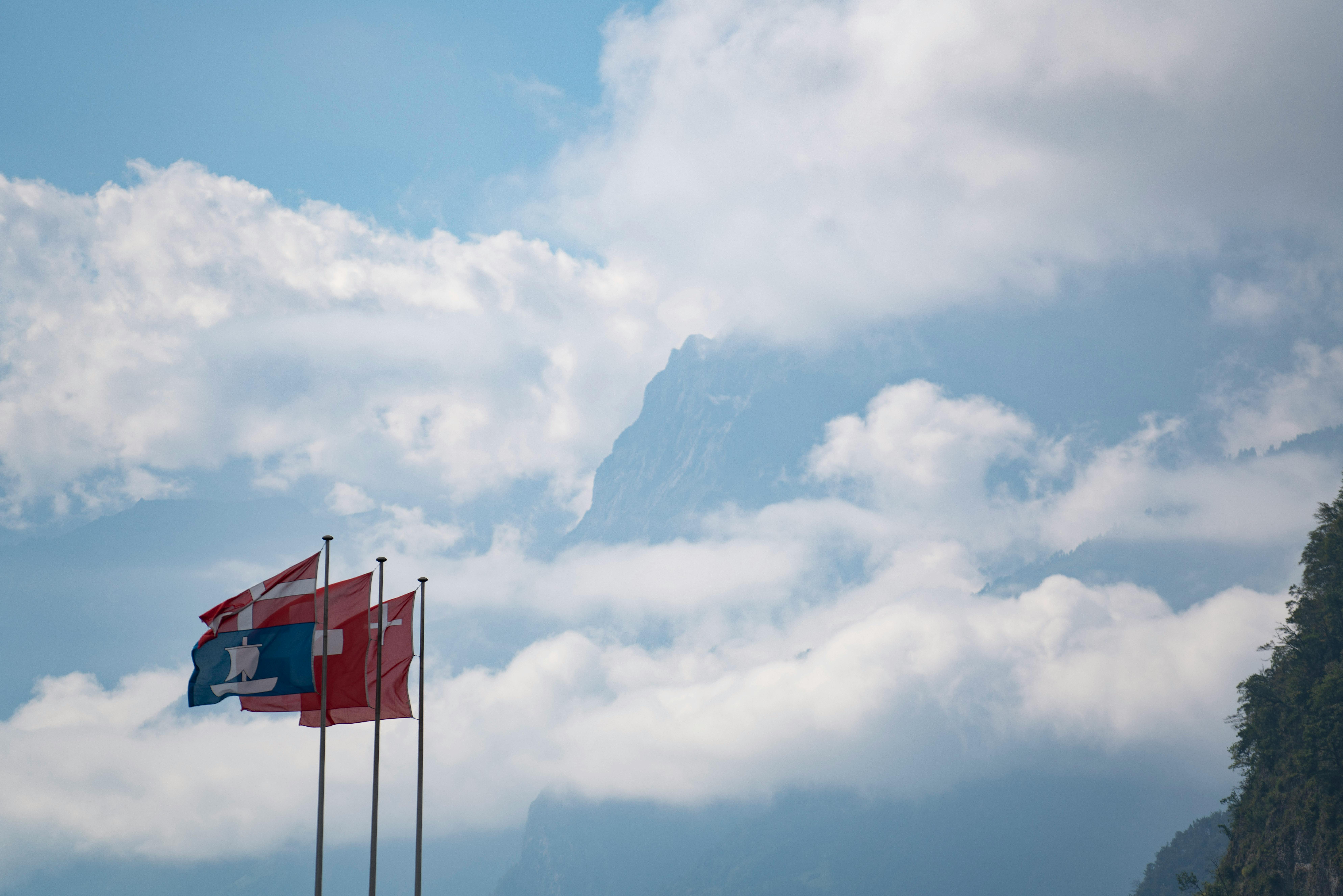 Swiss Flags Against Cloudy Alpine Backdrop · Free Stock Photo