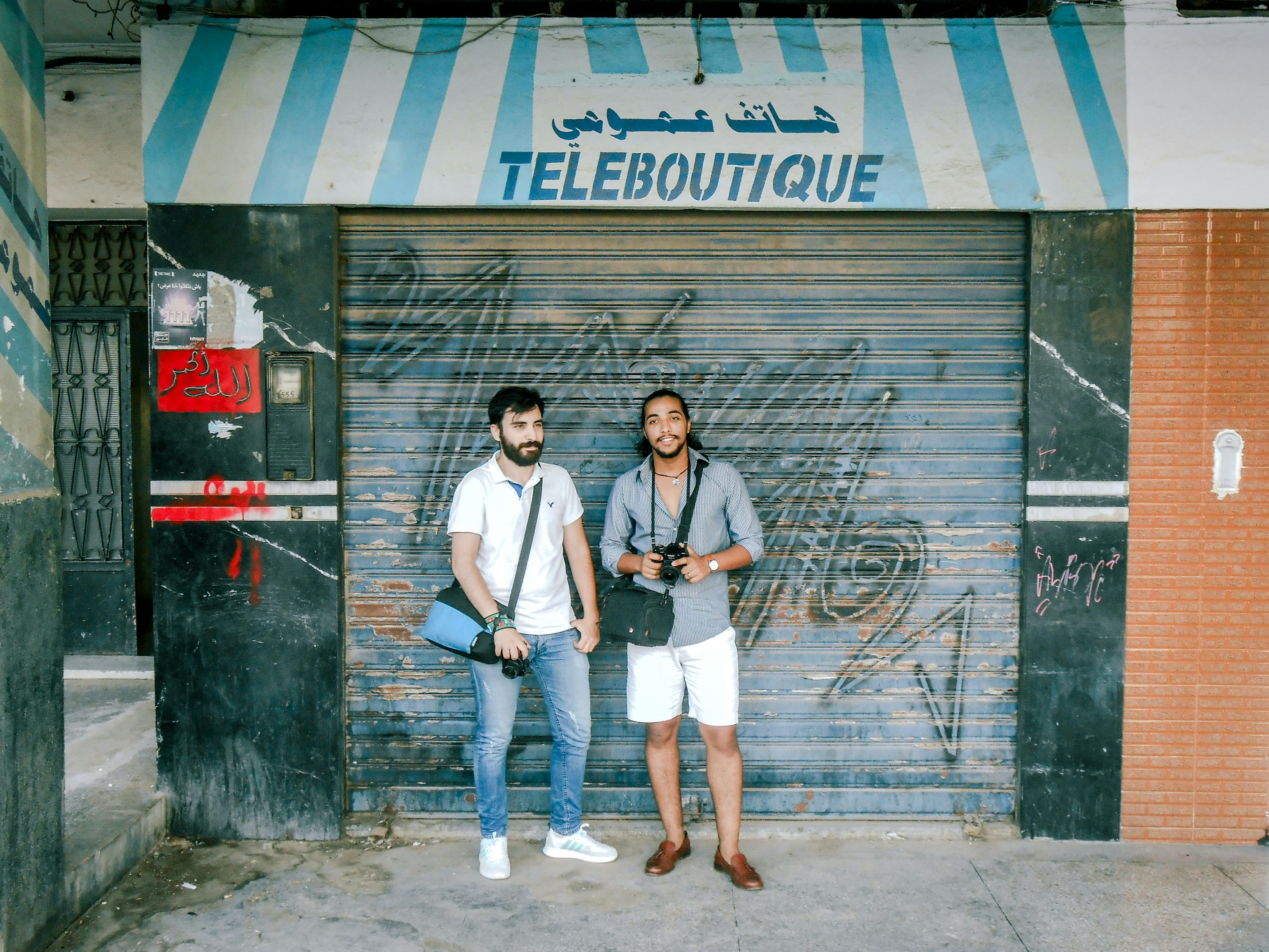 Two Men Posing Outside Teleboutique Storefront · Free Stock Photo