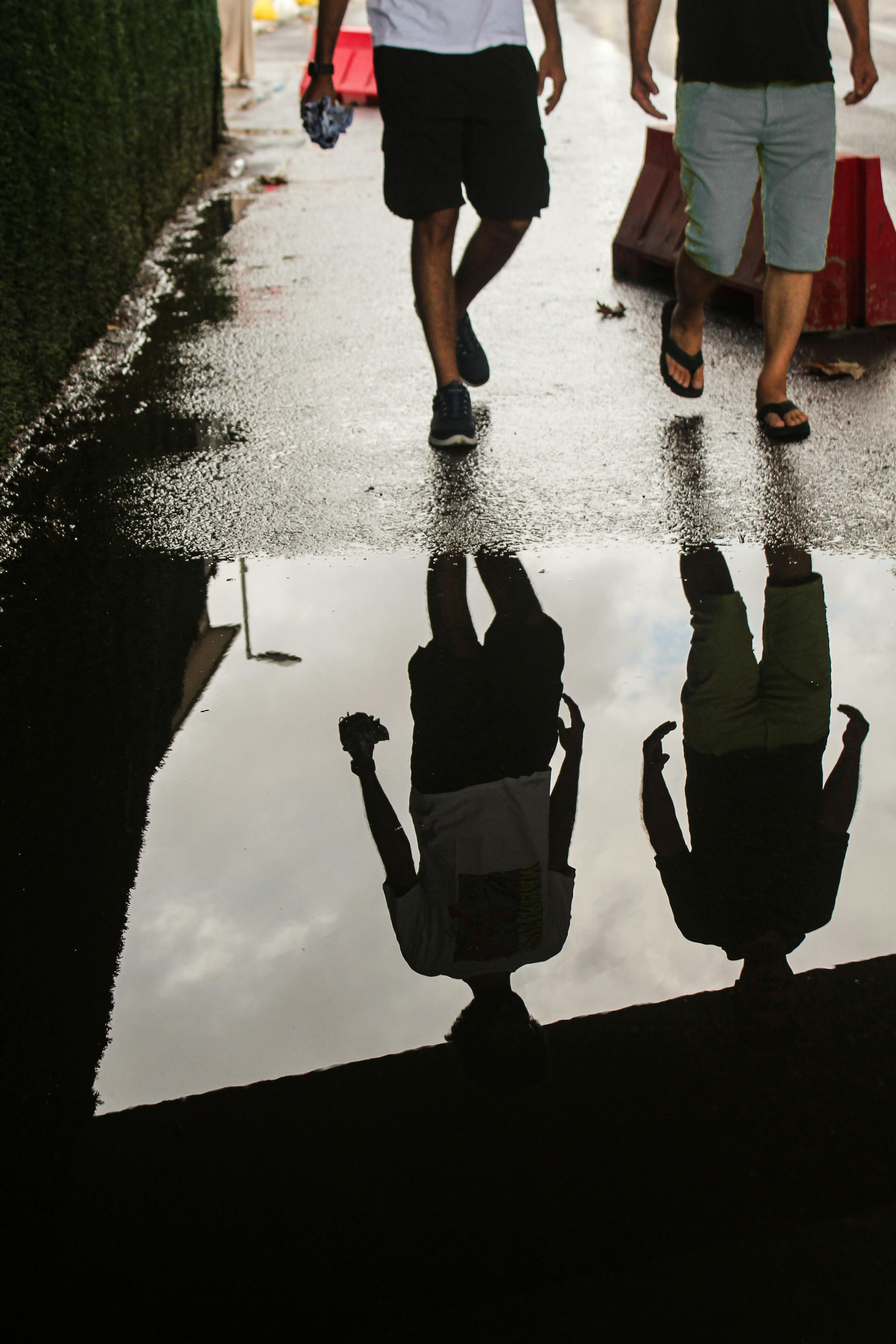 People Walking Reflected in Puddle on Street · Free Stock Photo