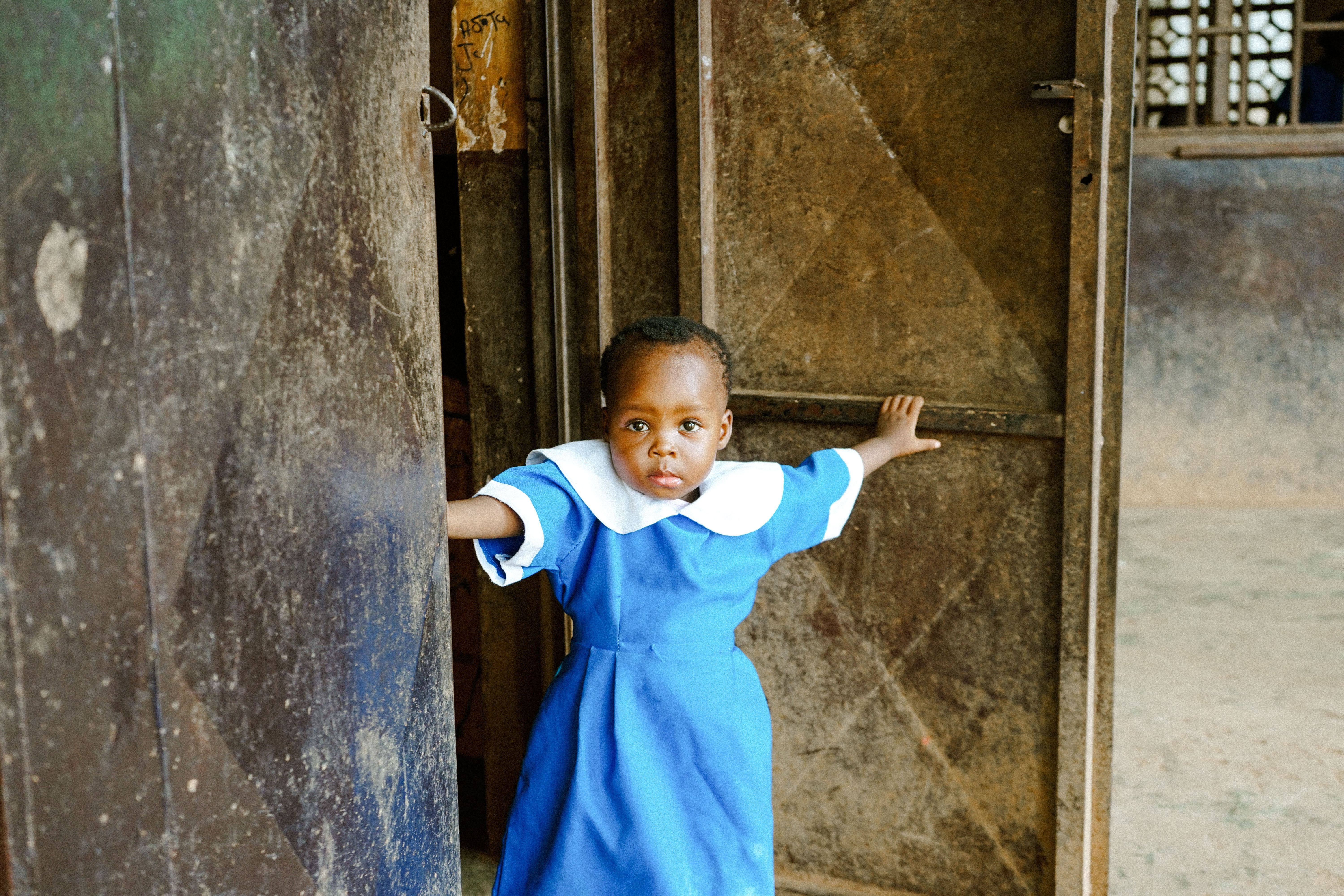 Young Child in Blue School Uniform Standing at Doorway · Free Stock Photo